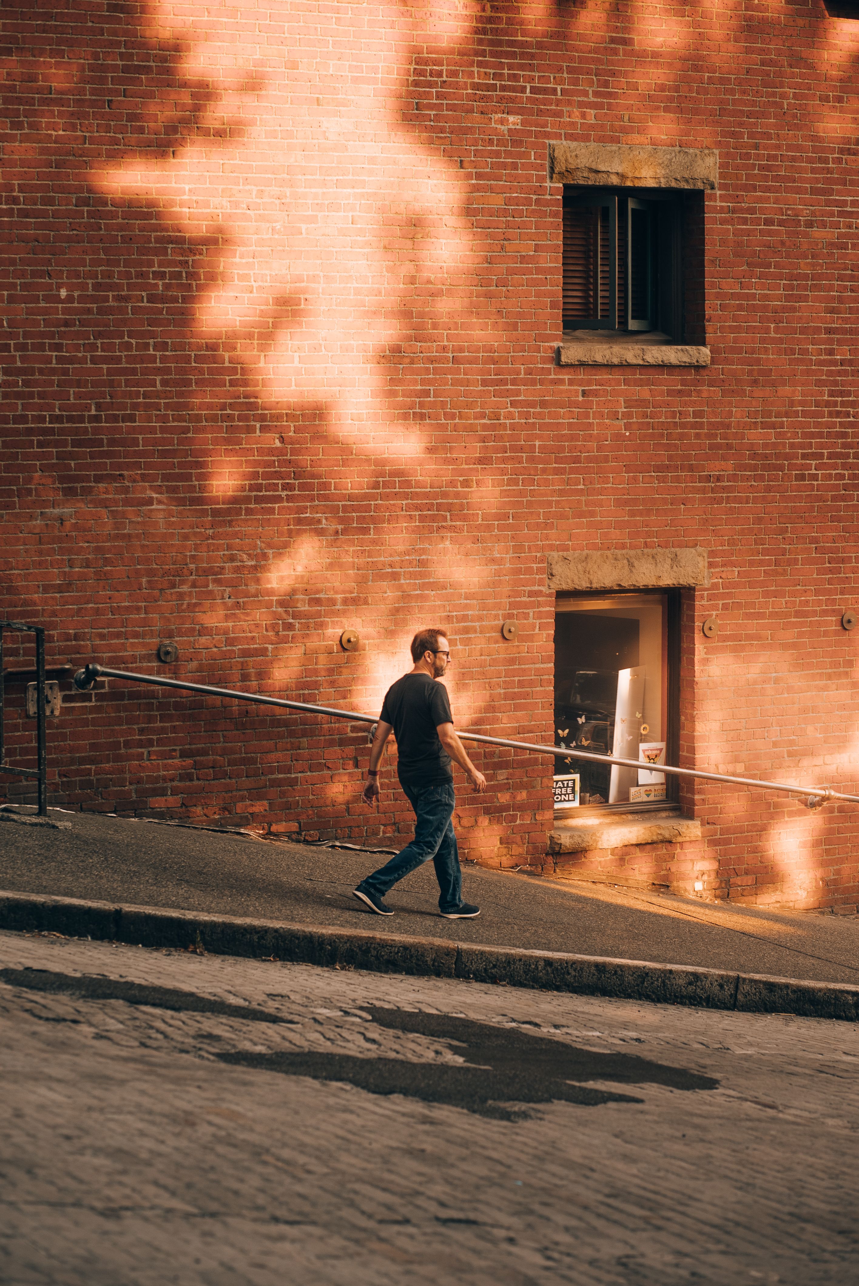 A man walking down a street in front of a brick building · Free Stock Photo