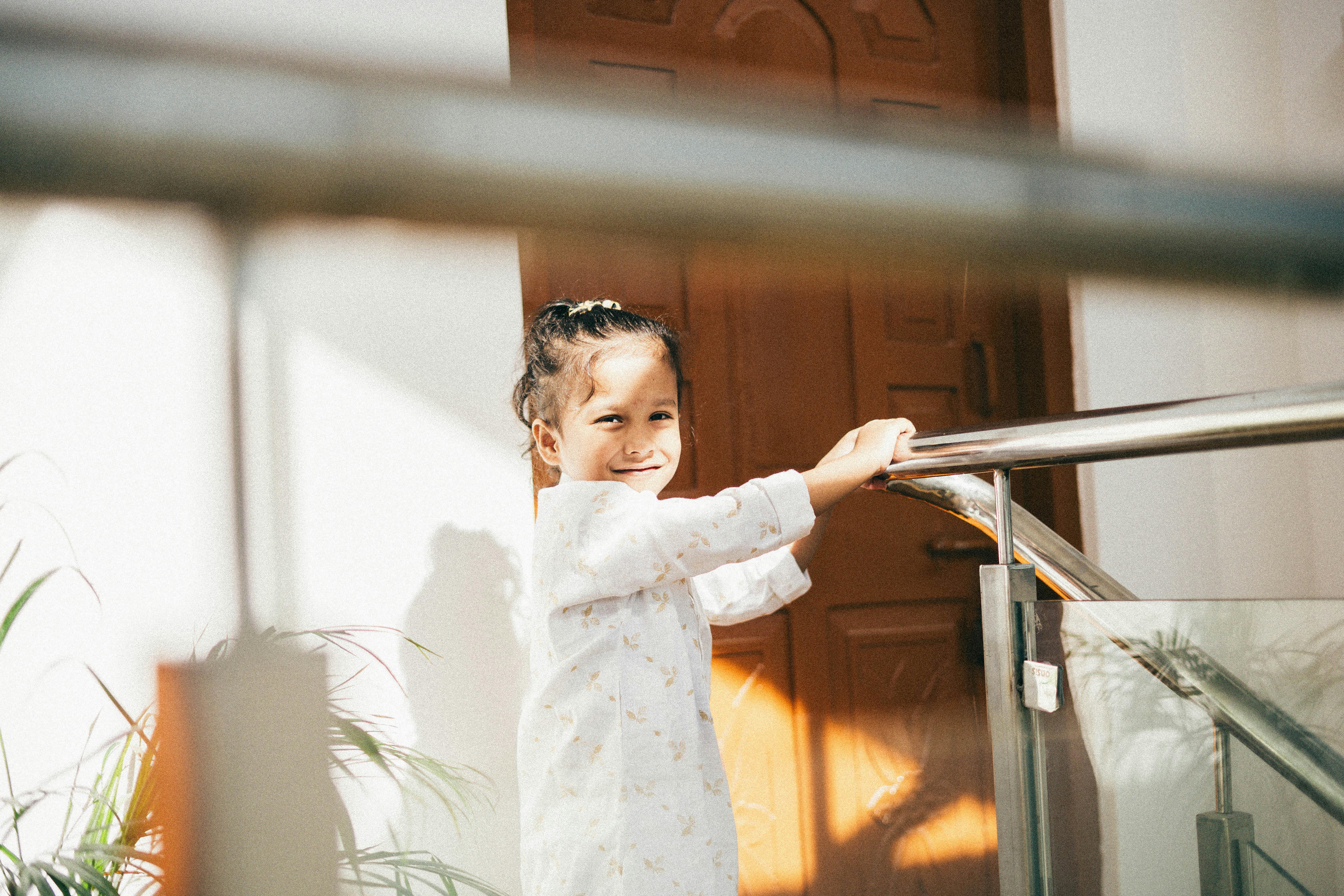 Portrait of a Little Girl Touching a Staircase Handrail · Free Stock Photo