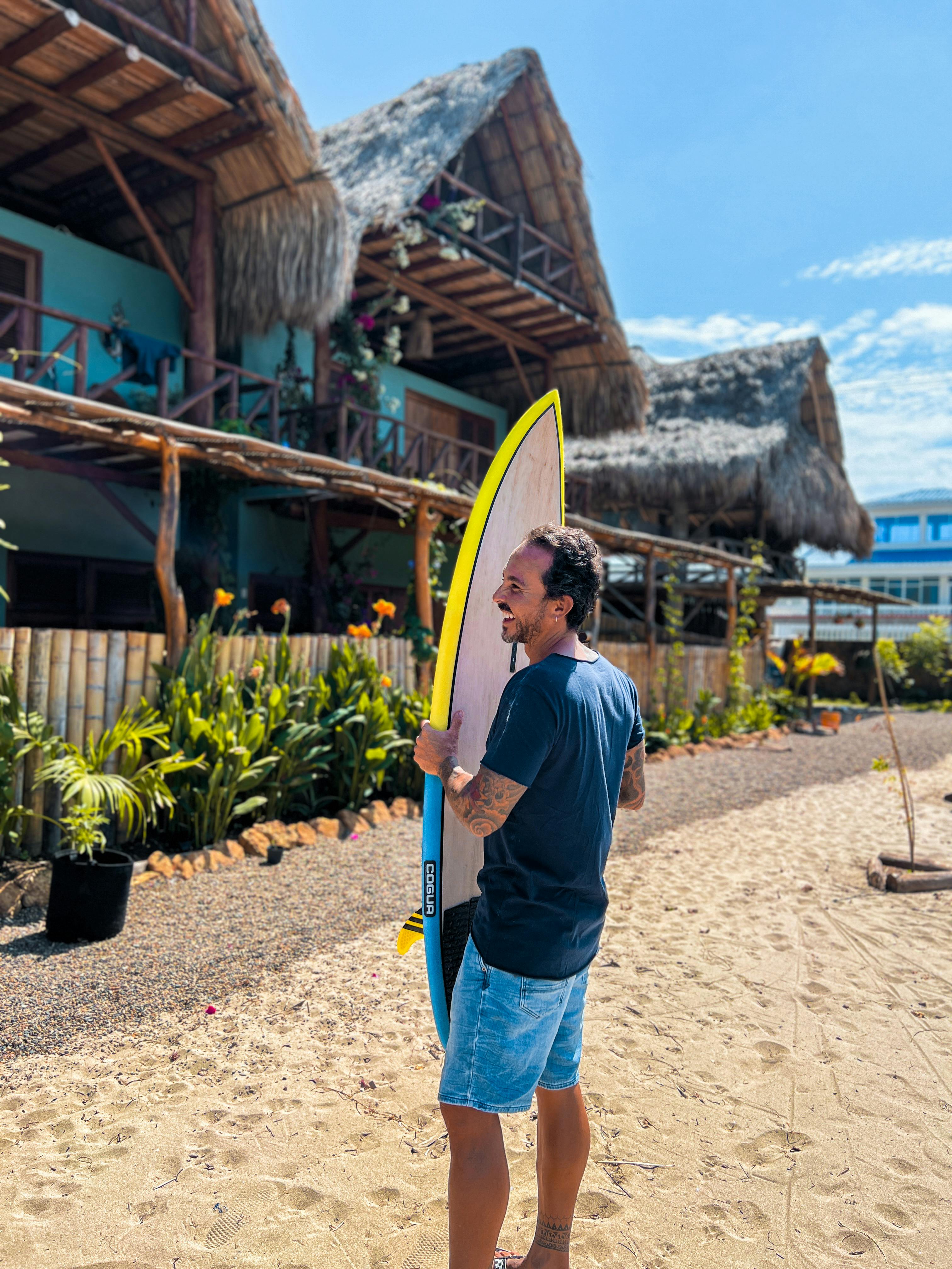 Smiling Surfer Standing near Houses on Beach · Free Stock Photo