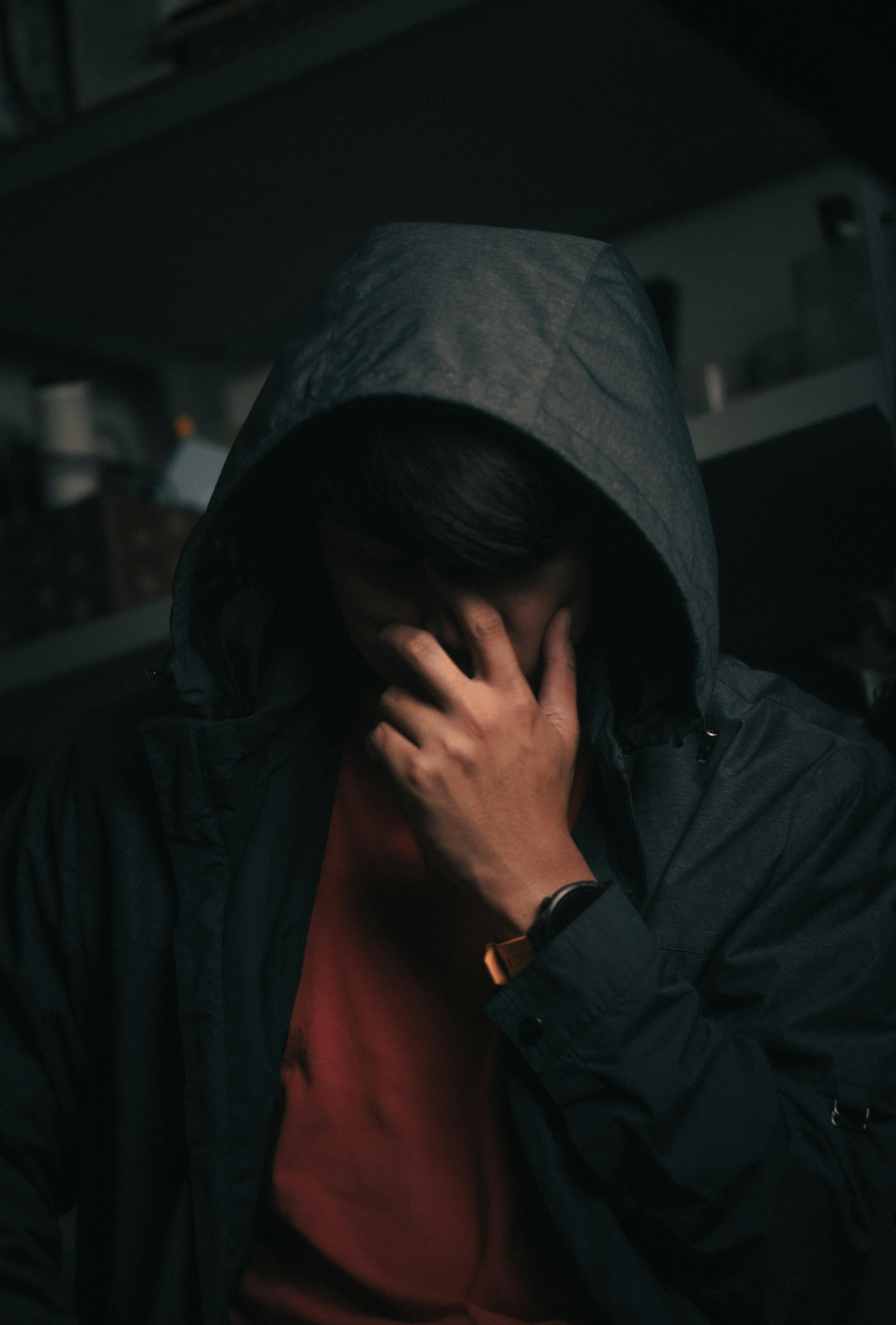 Man in Hooded Jacket Covering Face in Hand · Free Stock Photo