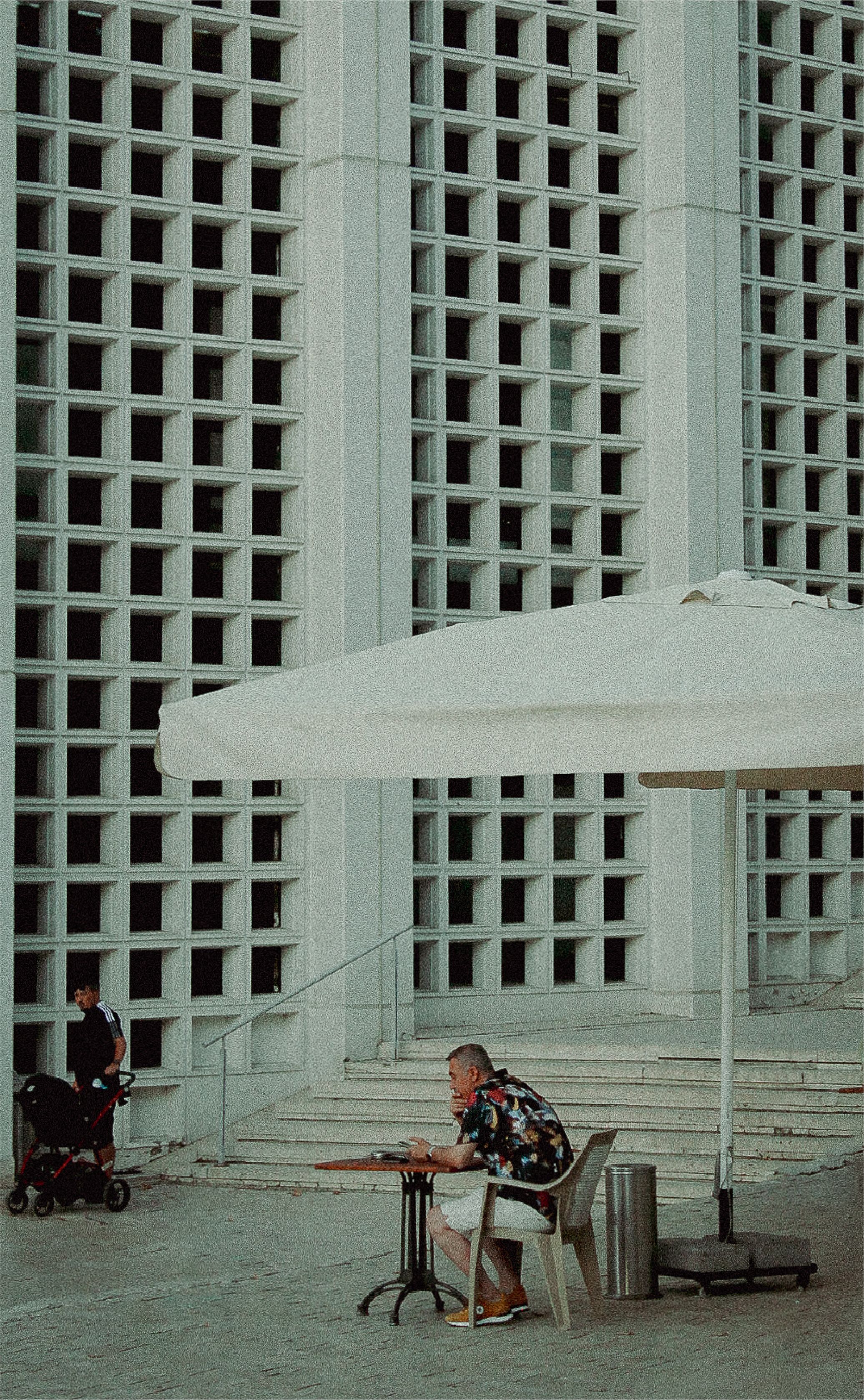 Man Sitting under Umbrella near White Building Wall · Free Stock Photo