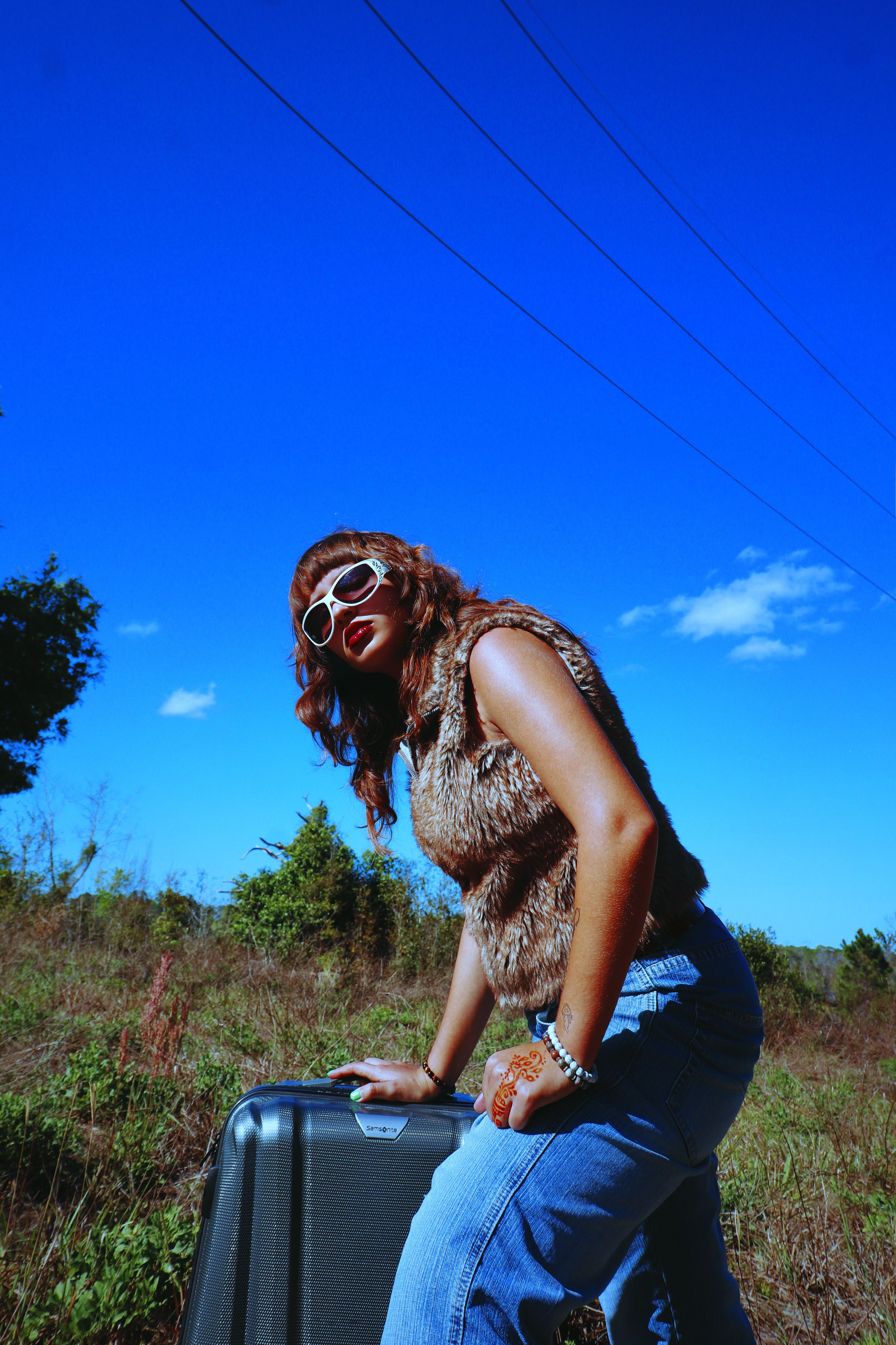 Woman in Sunglasses and Vest Standing with Suitcase · Free Stock Photo
