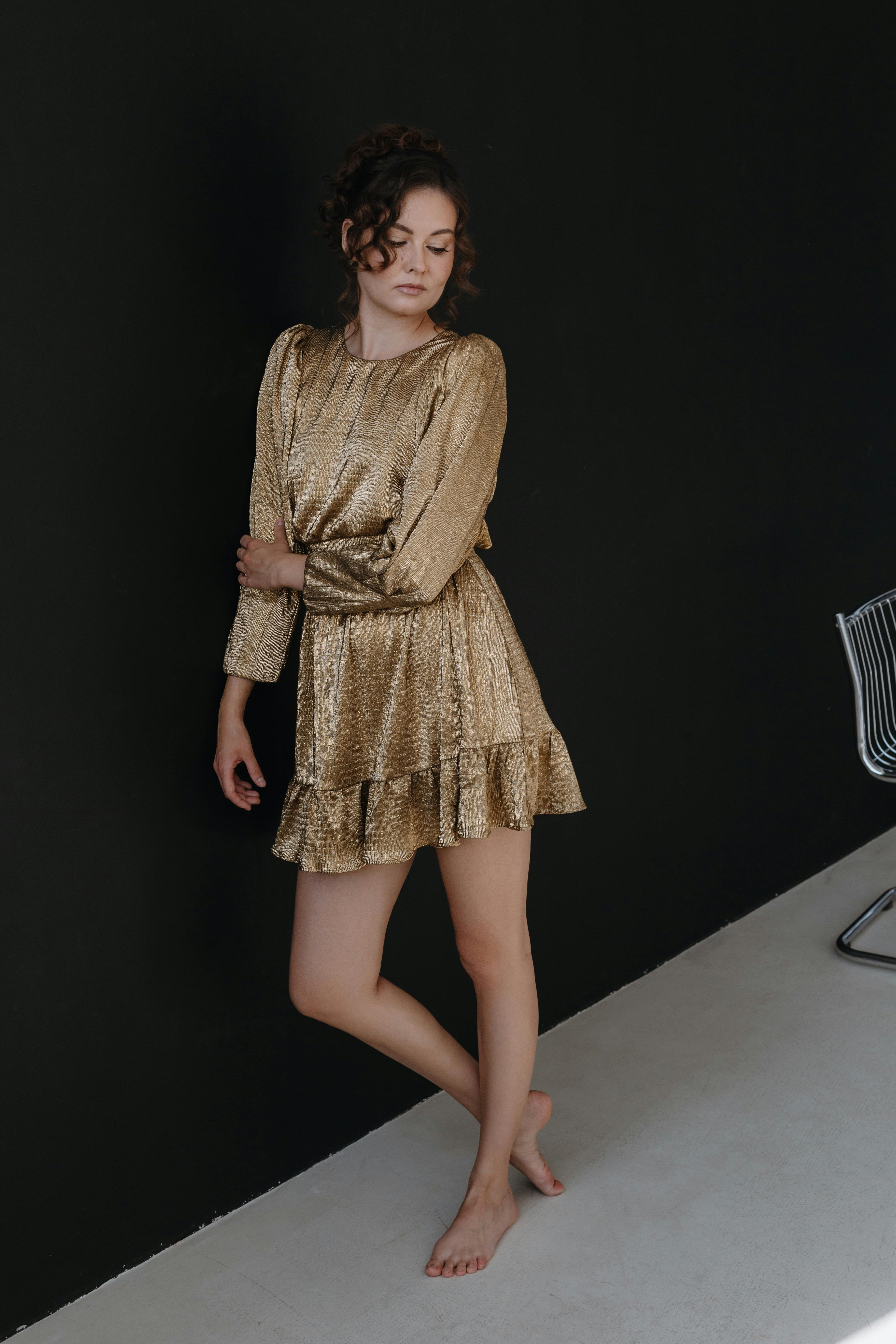 Woman in Golden Dress Leaning against Black Wall · Free Stock Photo