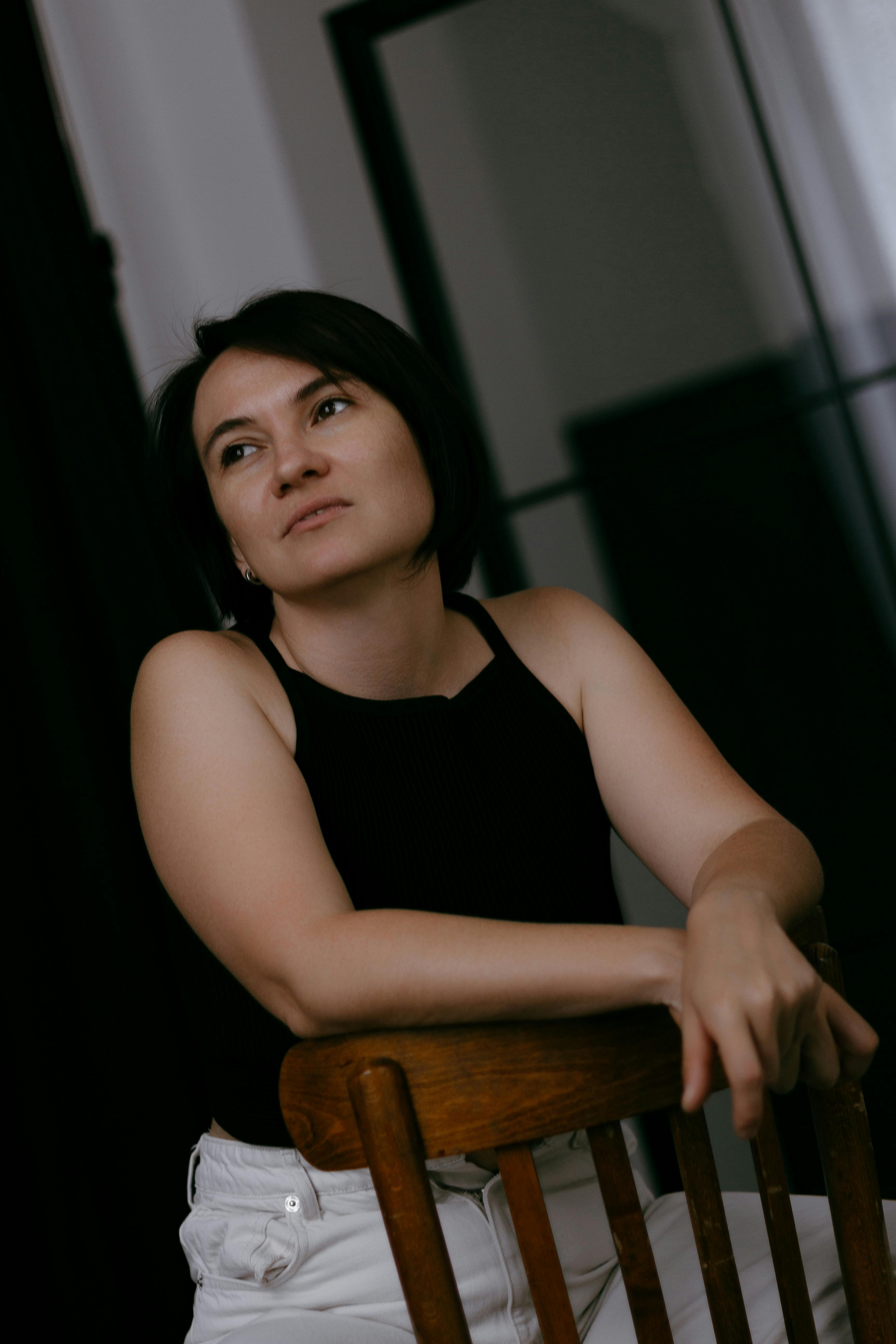 Woman in a Black Tank Top and White Pants Sitting Backwards on a Chair ...