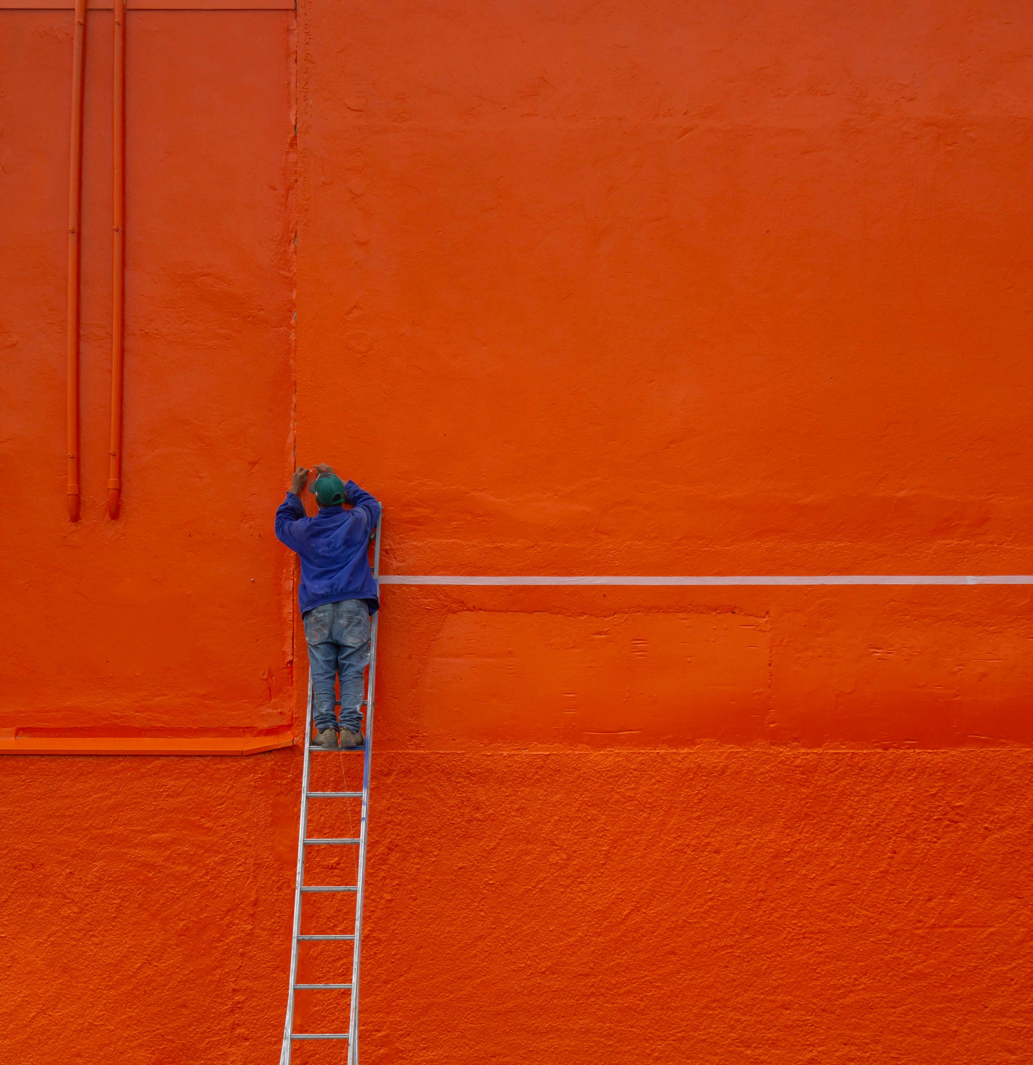 Man Standing on a Ladder in Front of an Orange Wall · Free Stock Photo