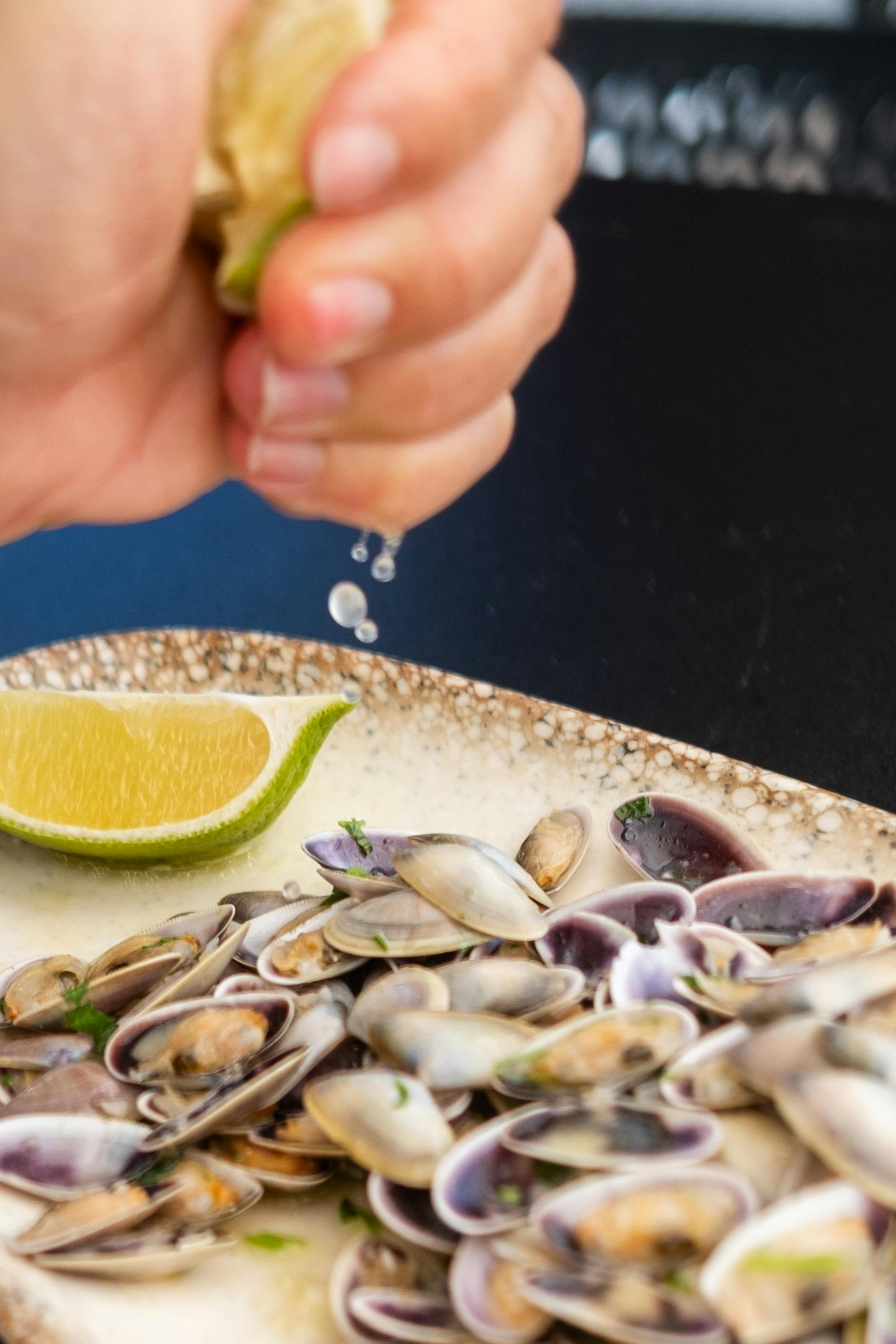 A person is squeezing lime on a clamshell · Free Stock Photo