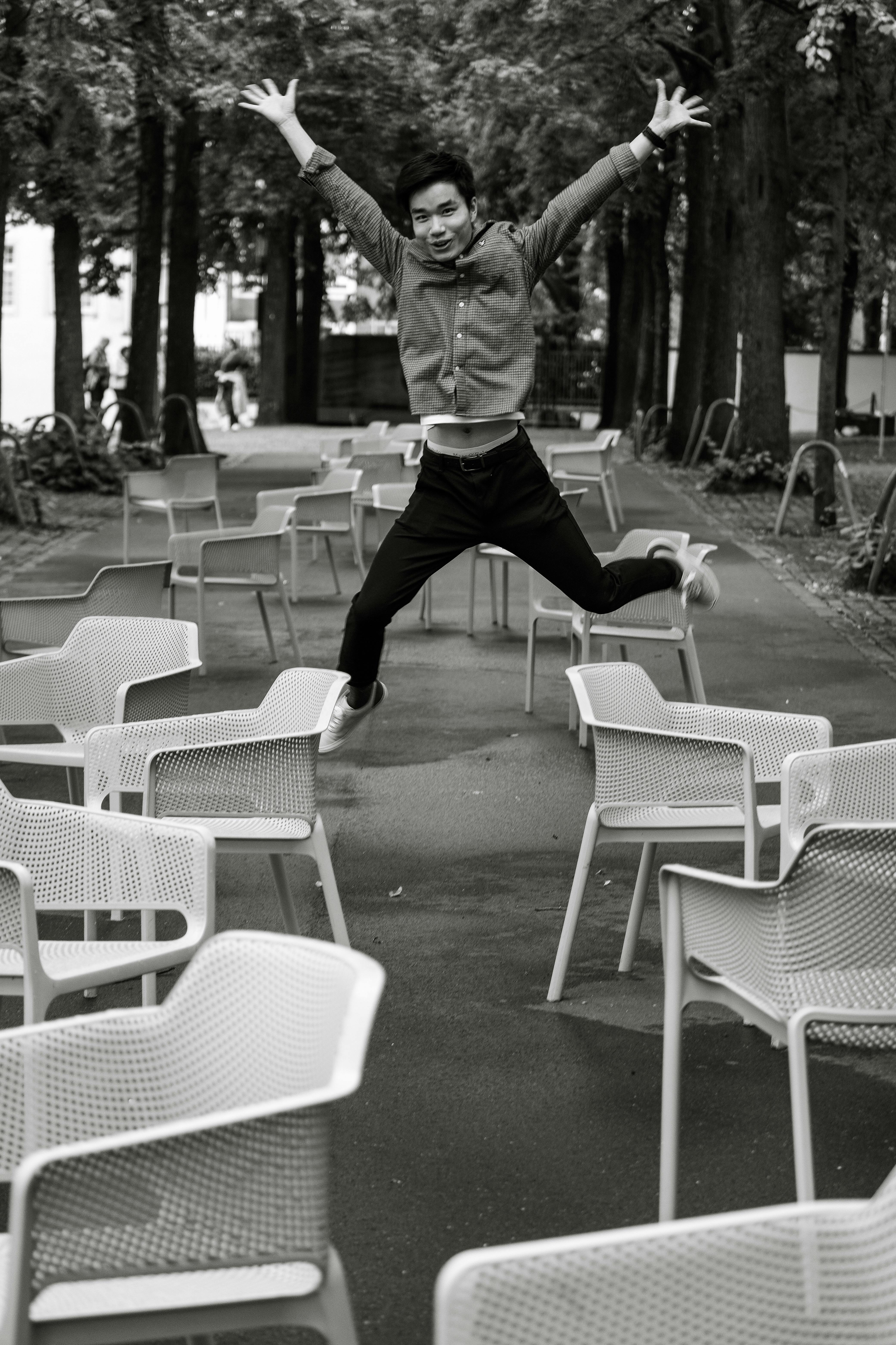 Man Jumping Among Chairs in Black and White · Free Stock Photo