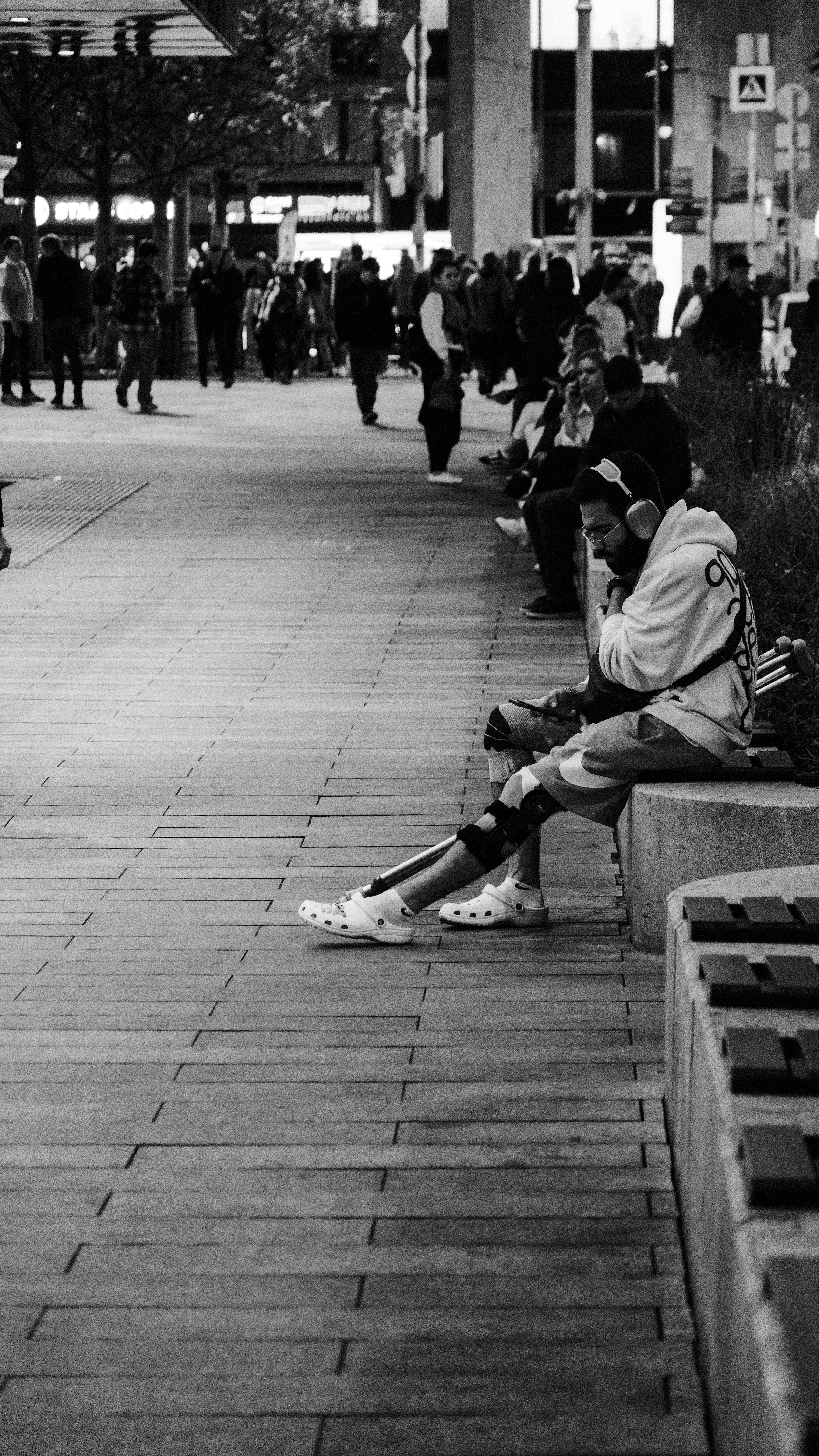 Man Sitting on a Bench by the Street in Grayscale · Free Stock Photo