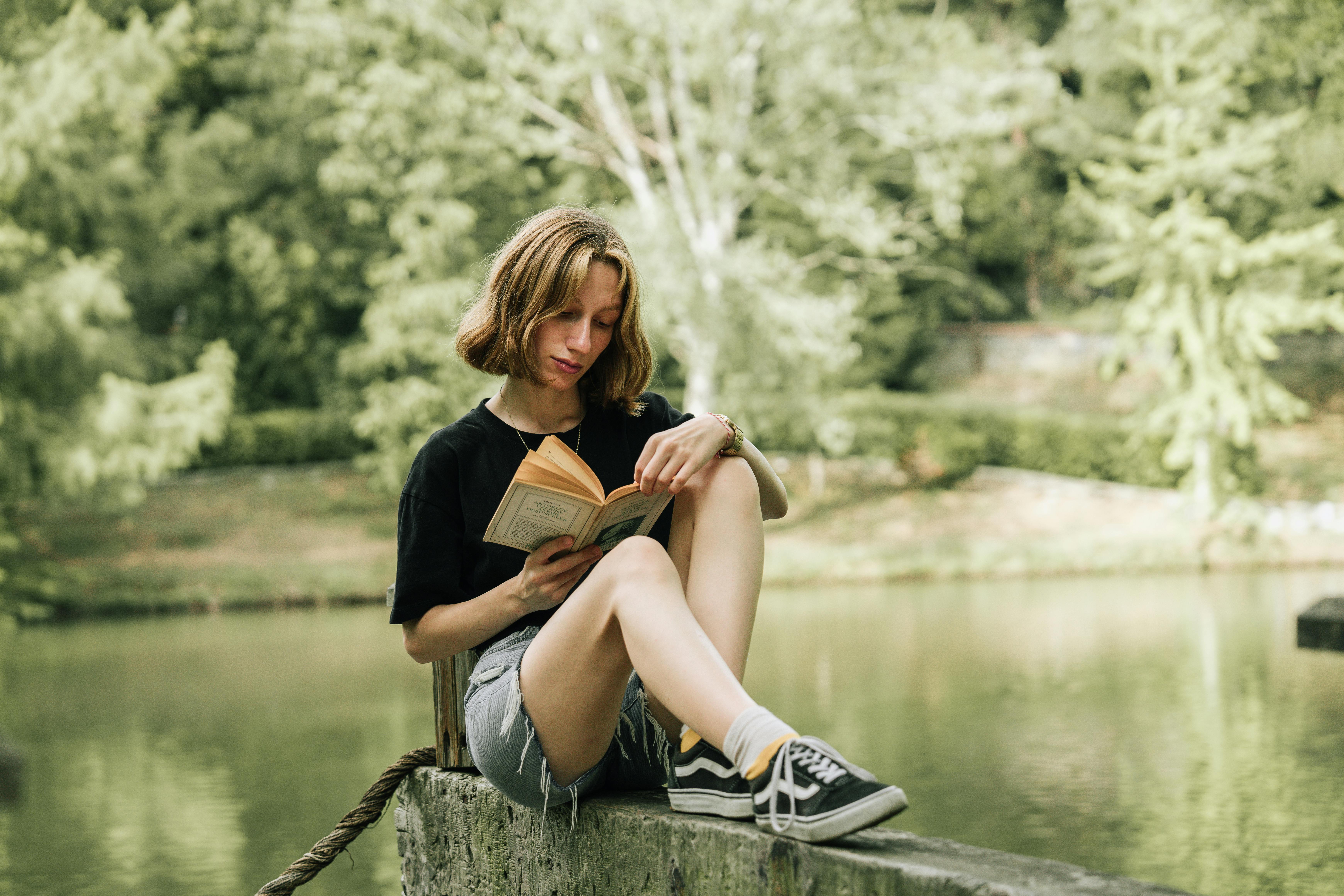 Woman Reading a Book Sitting on the Railing at the Lake · Free Stock Photo