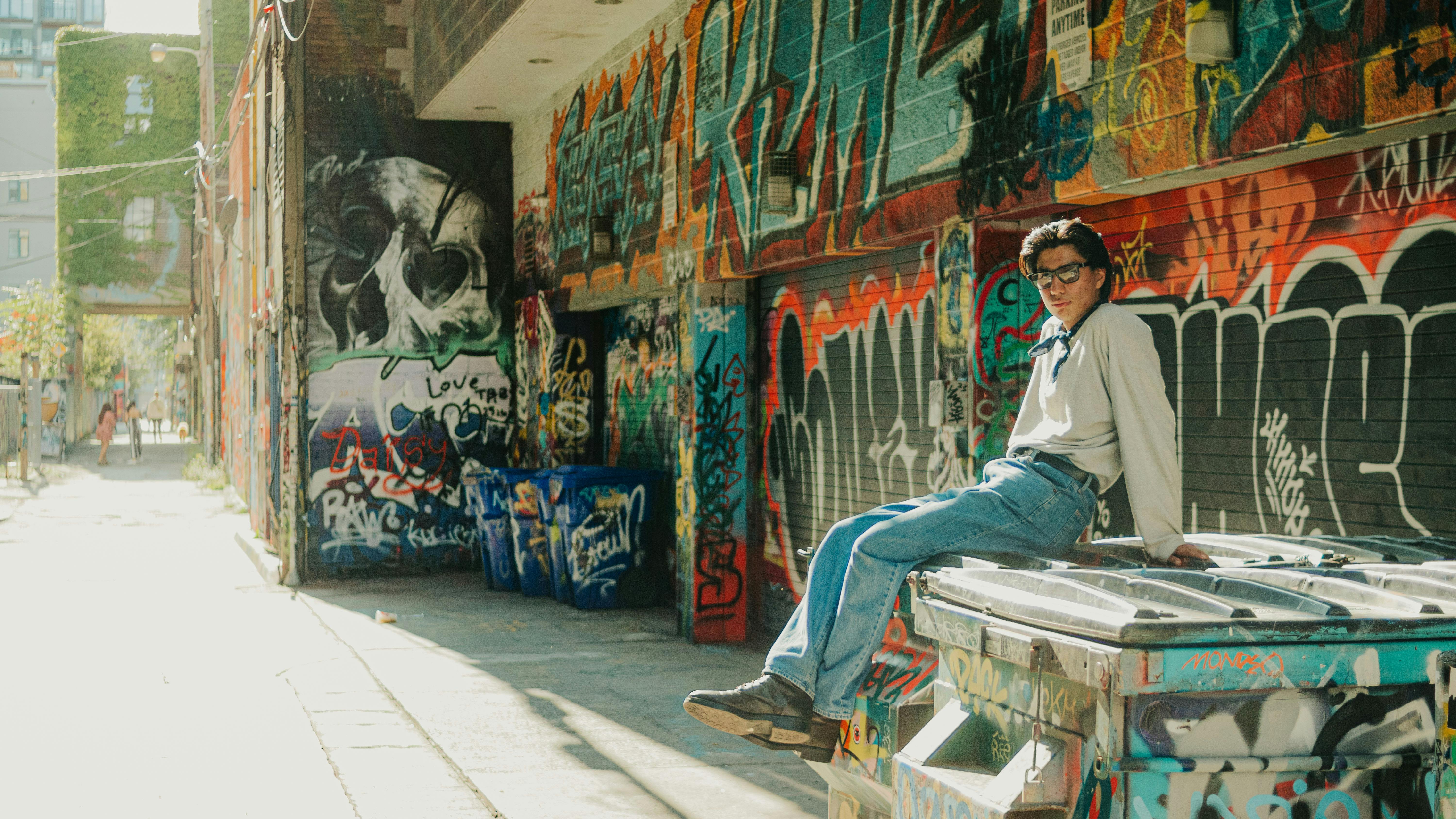 Man Sitting on the Background of a Wall with Graffiti · Free Stock Photo