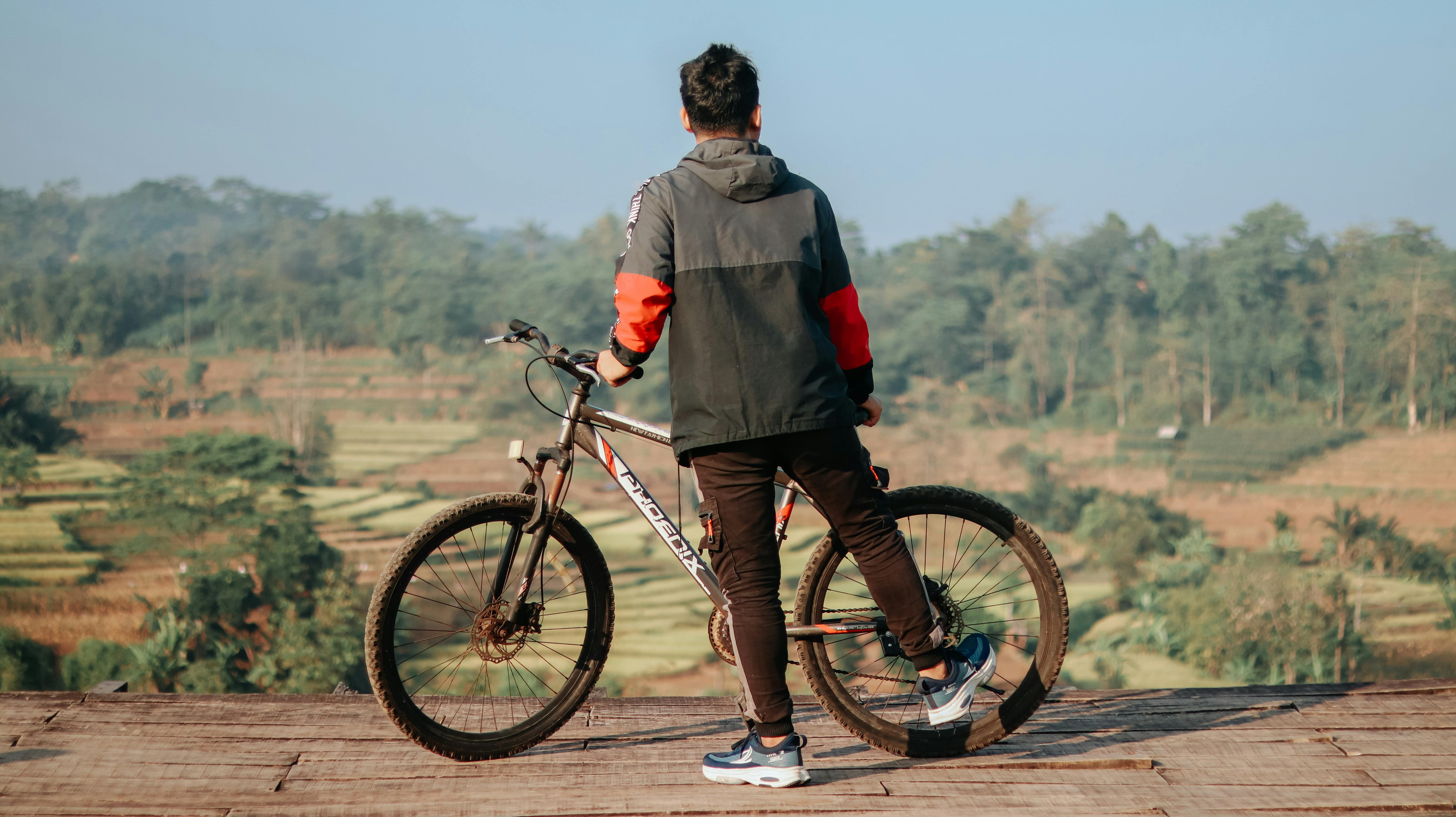 Man Standing with Bike in Rural Landscape · Free Stock Photo