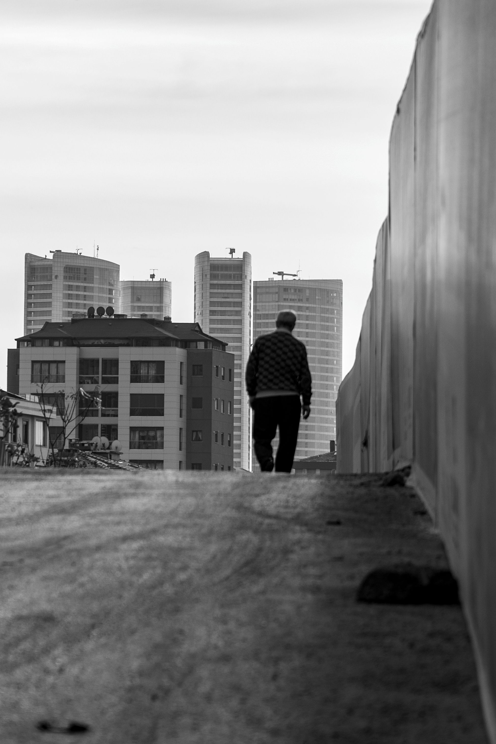 Man Walking along Wall against Residential Skyscrapers · Free Stock Photo