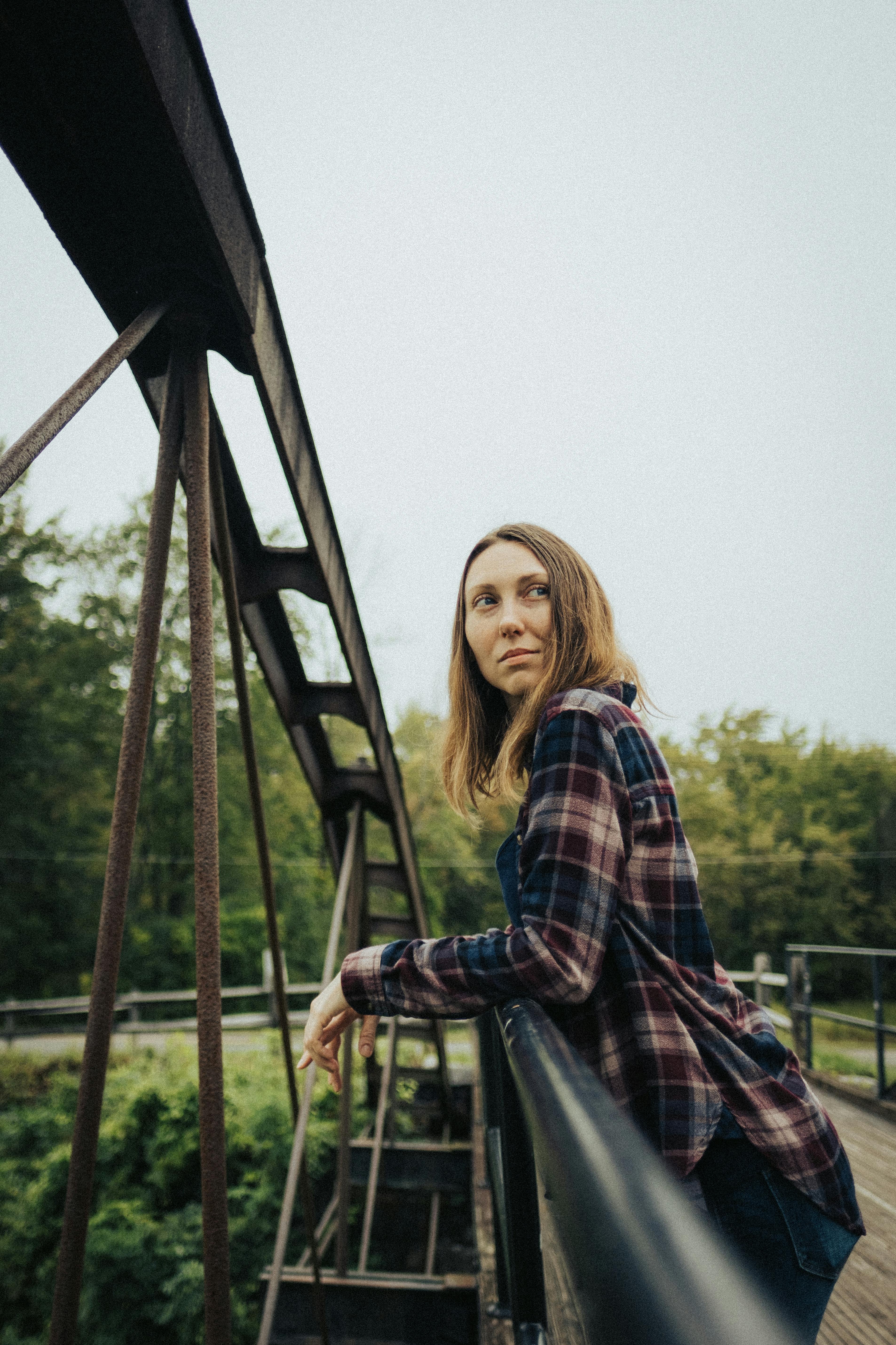 Woman in Check Shirt Leans on Bridge Handrail · Free Stock Photo