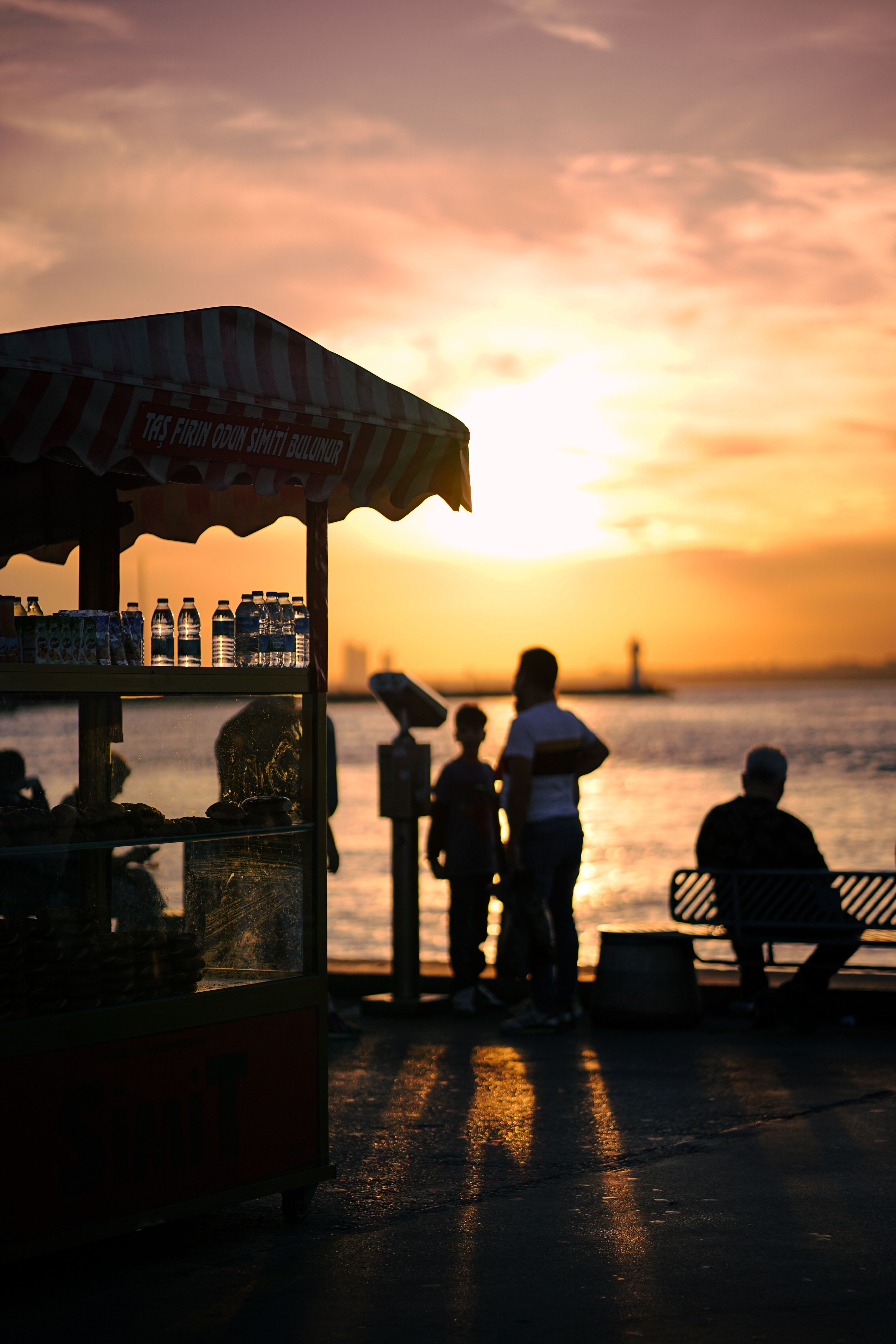 Person Standing on Sea Shore with People in Boat behind at Sunset ...