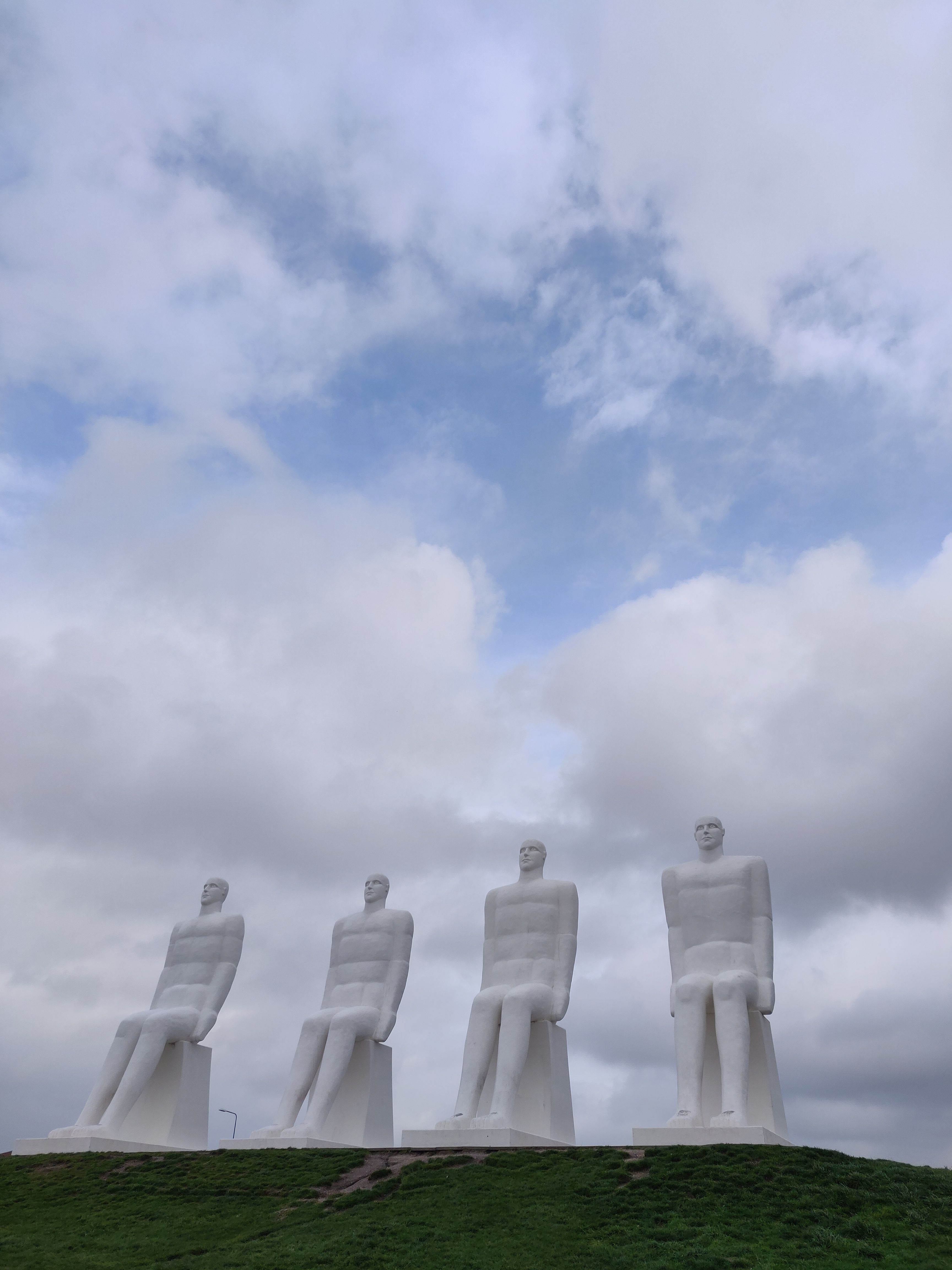 White Statues of Men Sitting in a Row against the Sky with Clouds ...