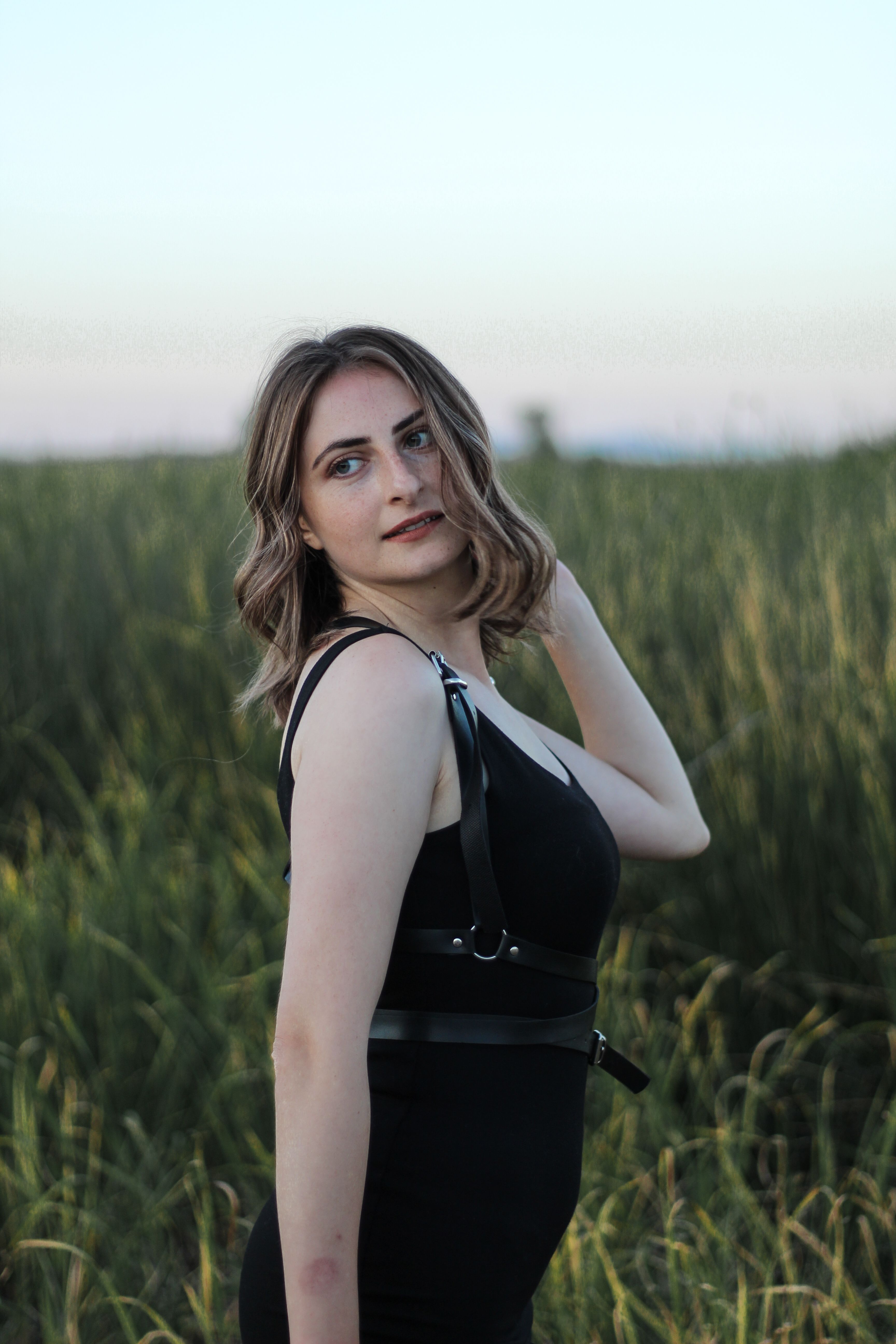 Woman in Black Strap Dress and Leather Harness Standing in Tall Grass ...