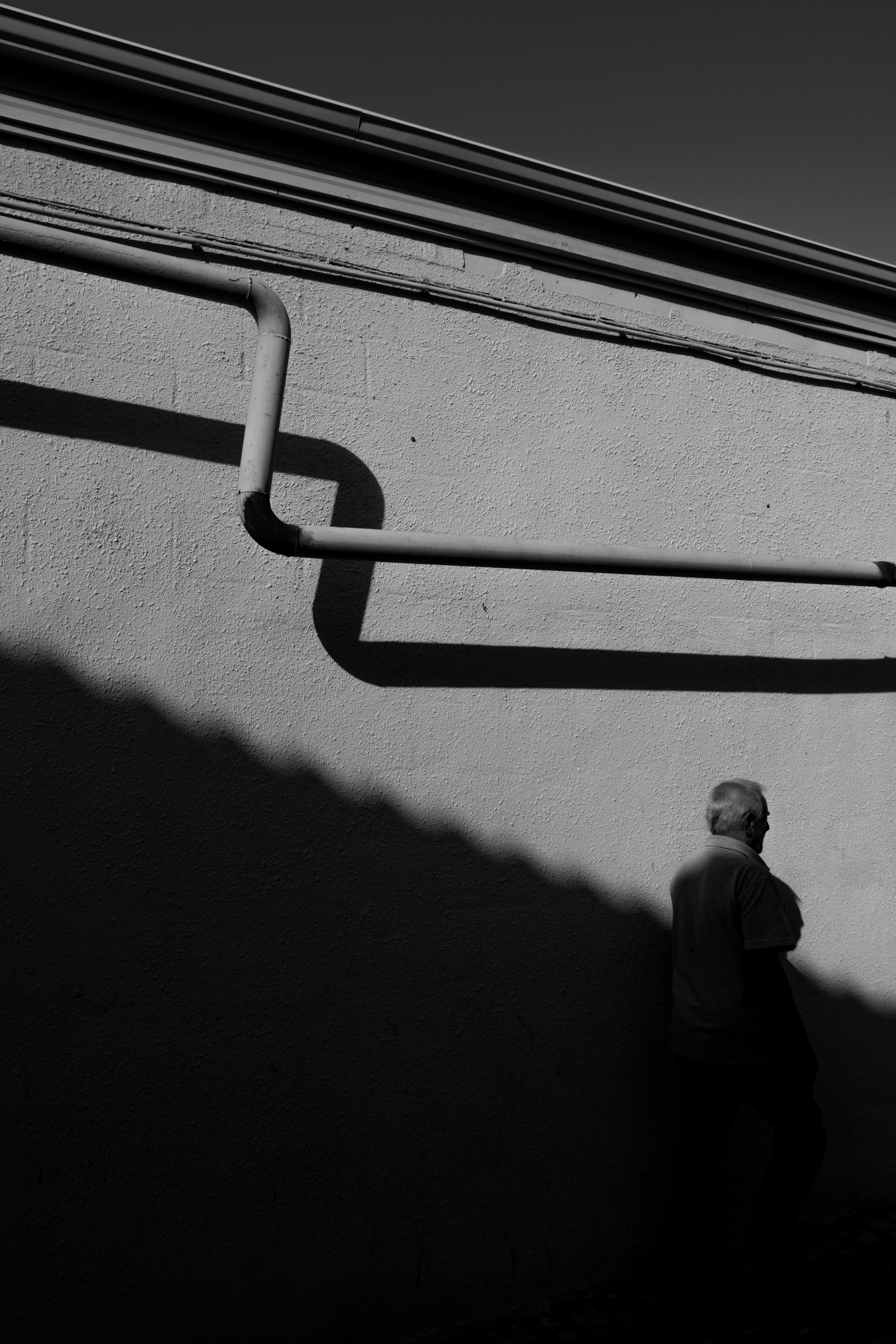 Man Standing in Shadow under Pipe on Wall · Free Stock Photo