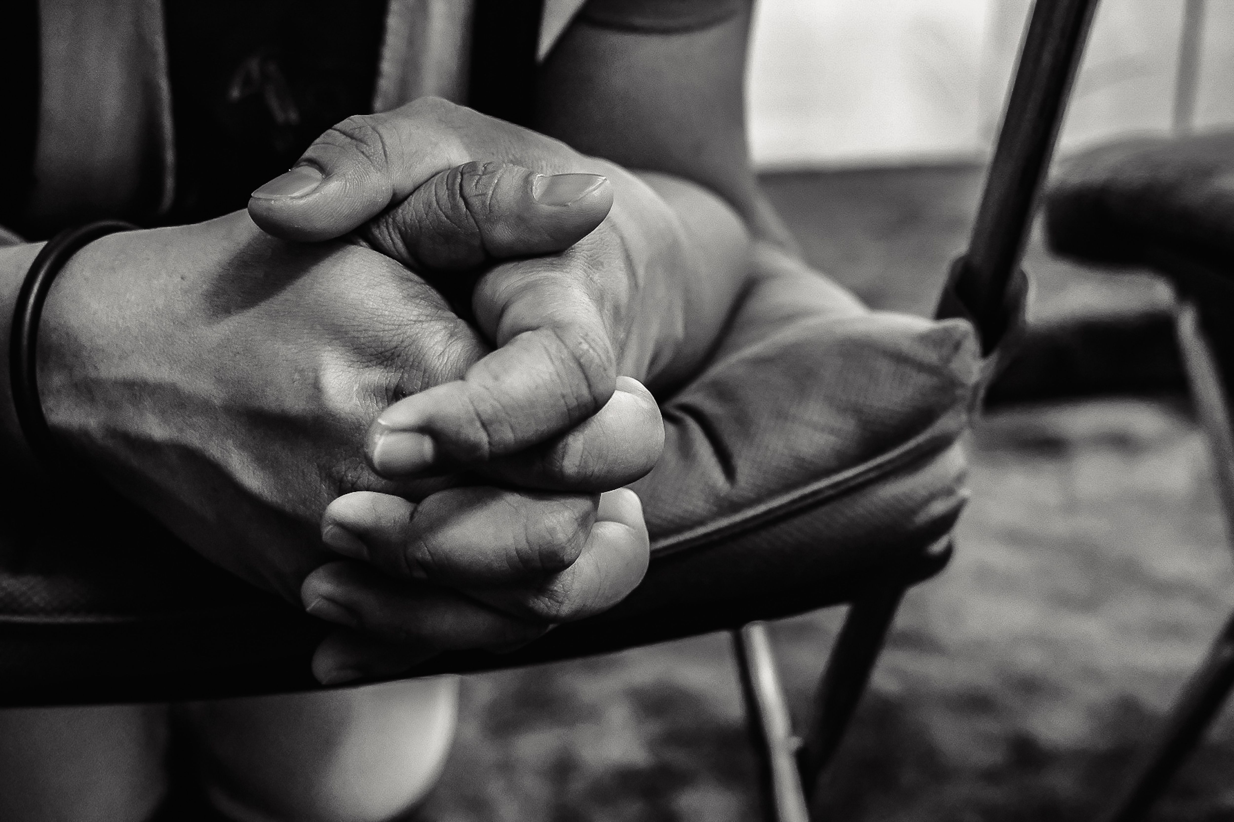 Black and White Photo of Hands Clasped Together Resting on Chair Seat ...