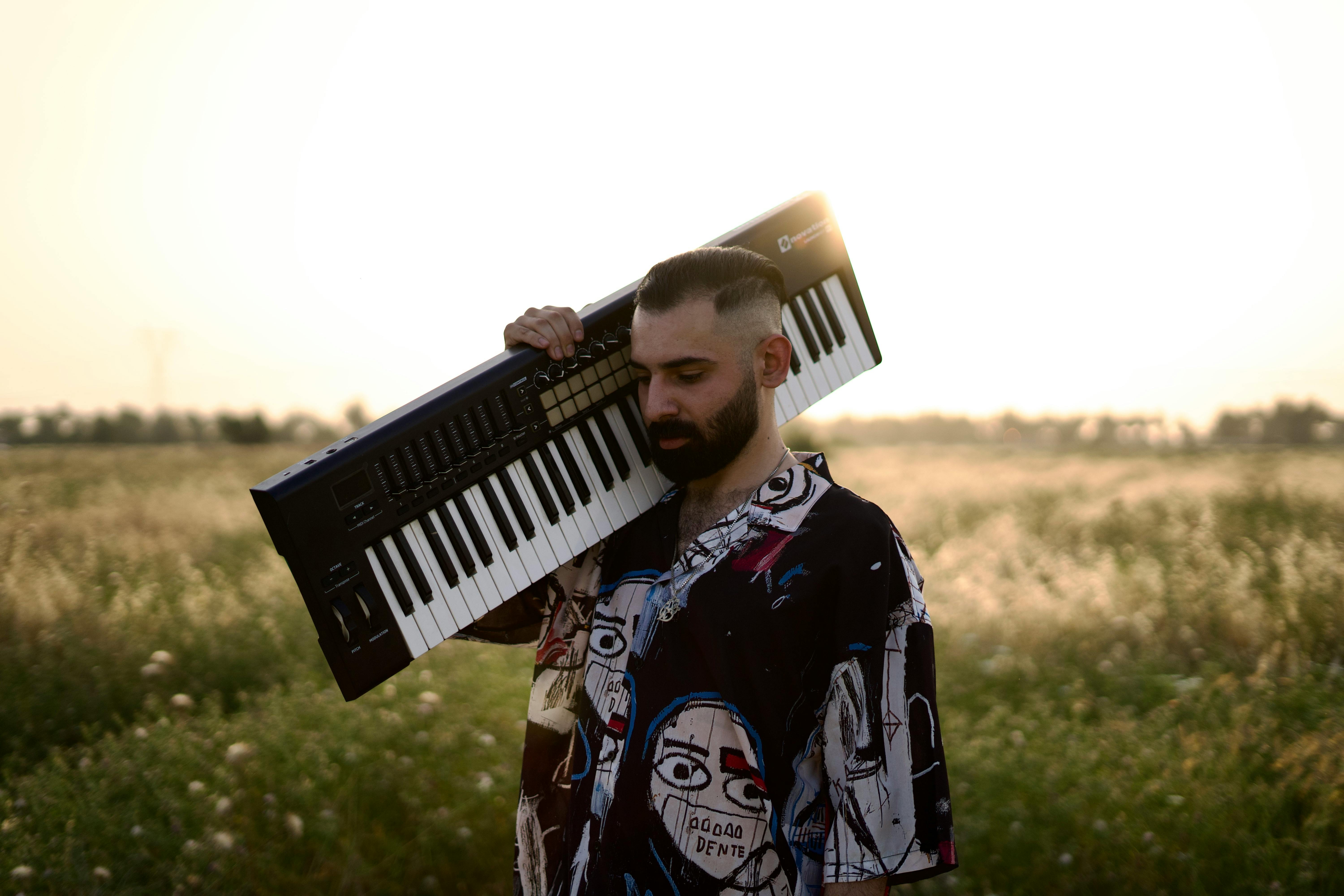 Man Carrying a Keyboard Controller on His Shoulder Walking in a Meadow ...