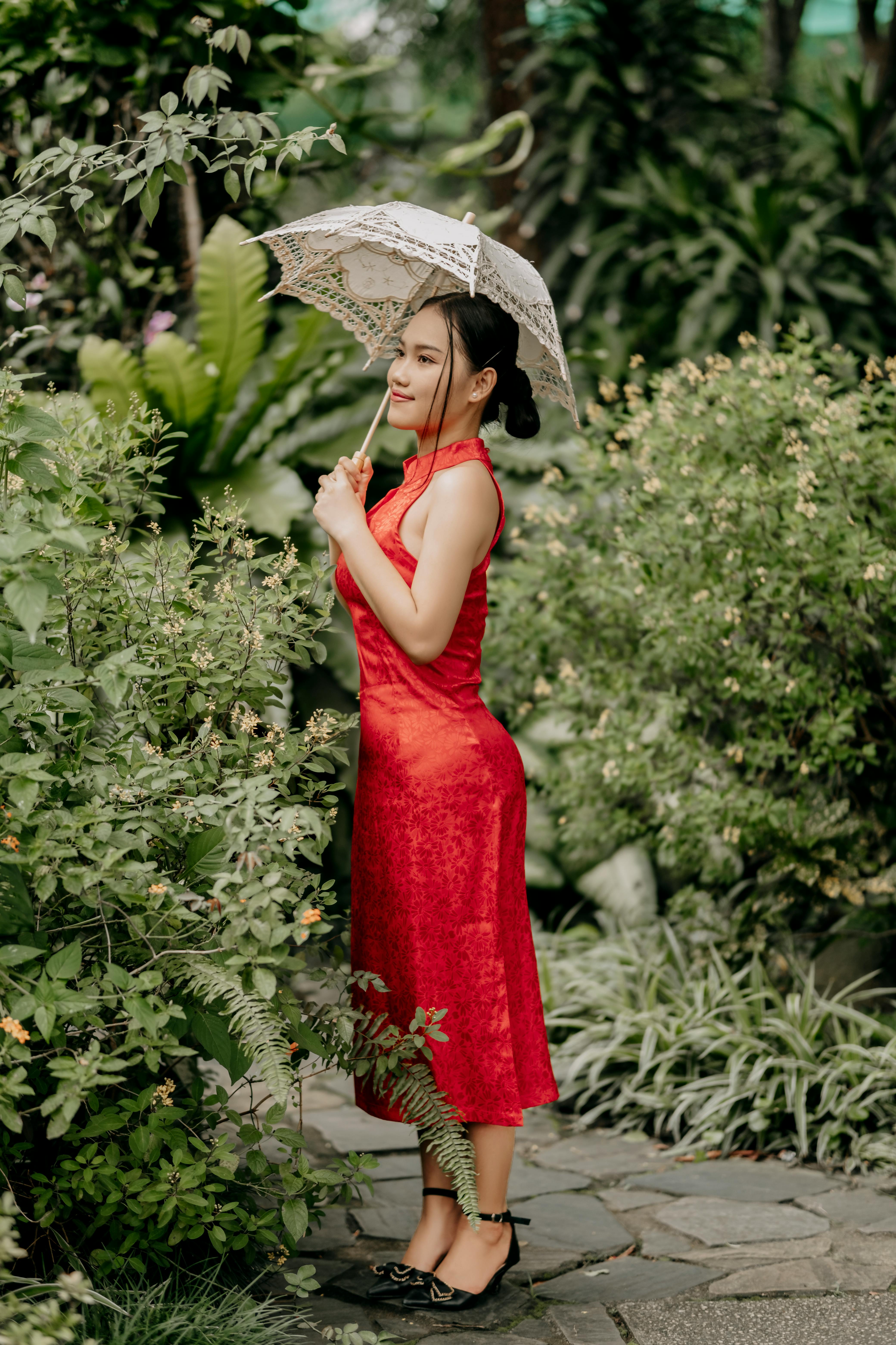 Model in Red Sleeveless Qipao Dress Under Small Sun Umbrella by a Shrub ...