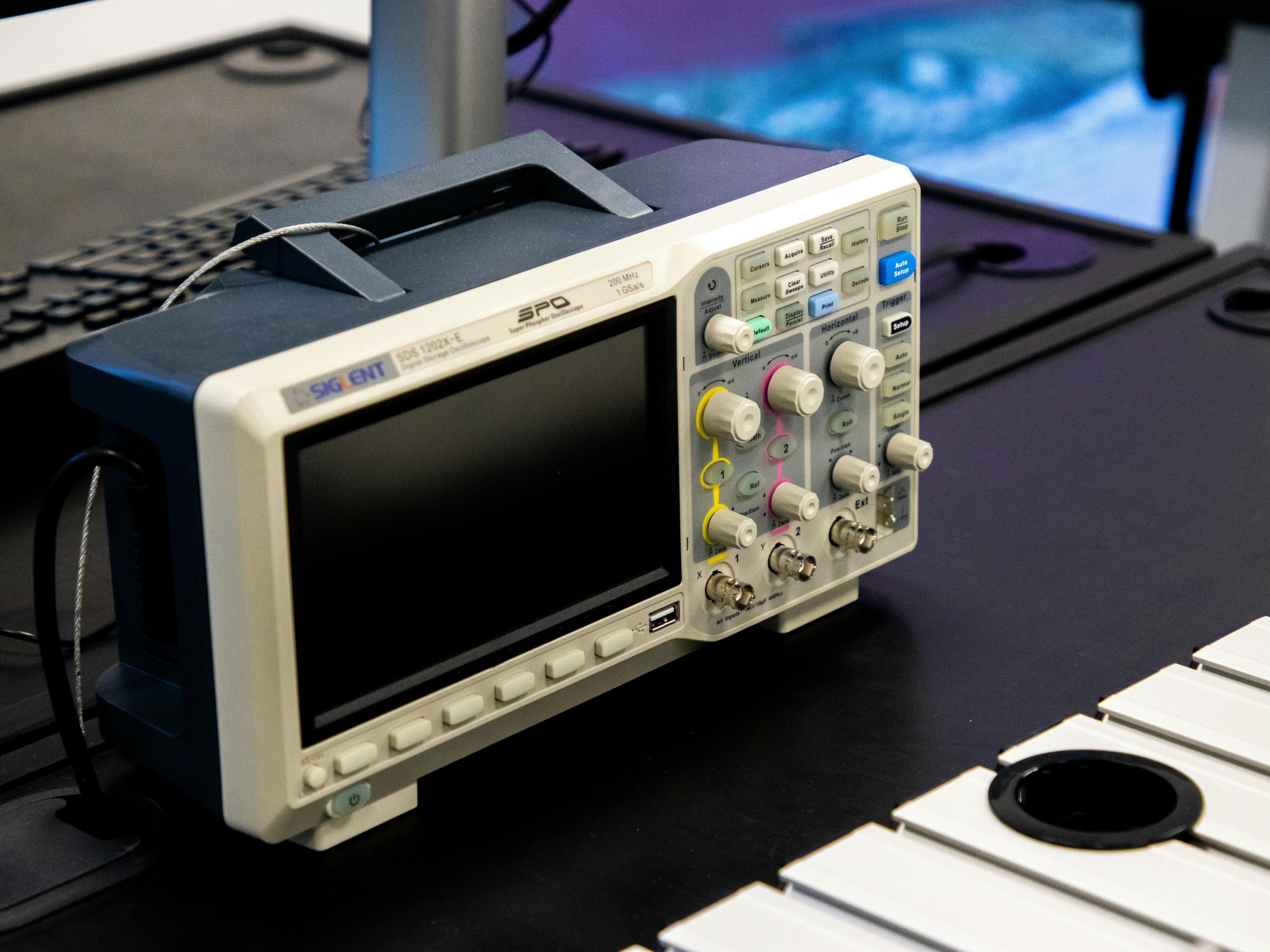 A digital oscilloscope on a table with a keyboard · Free Stock Photo