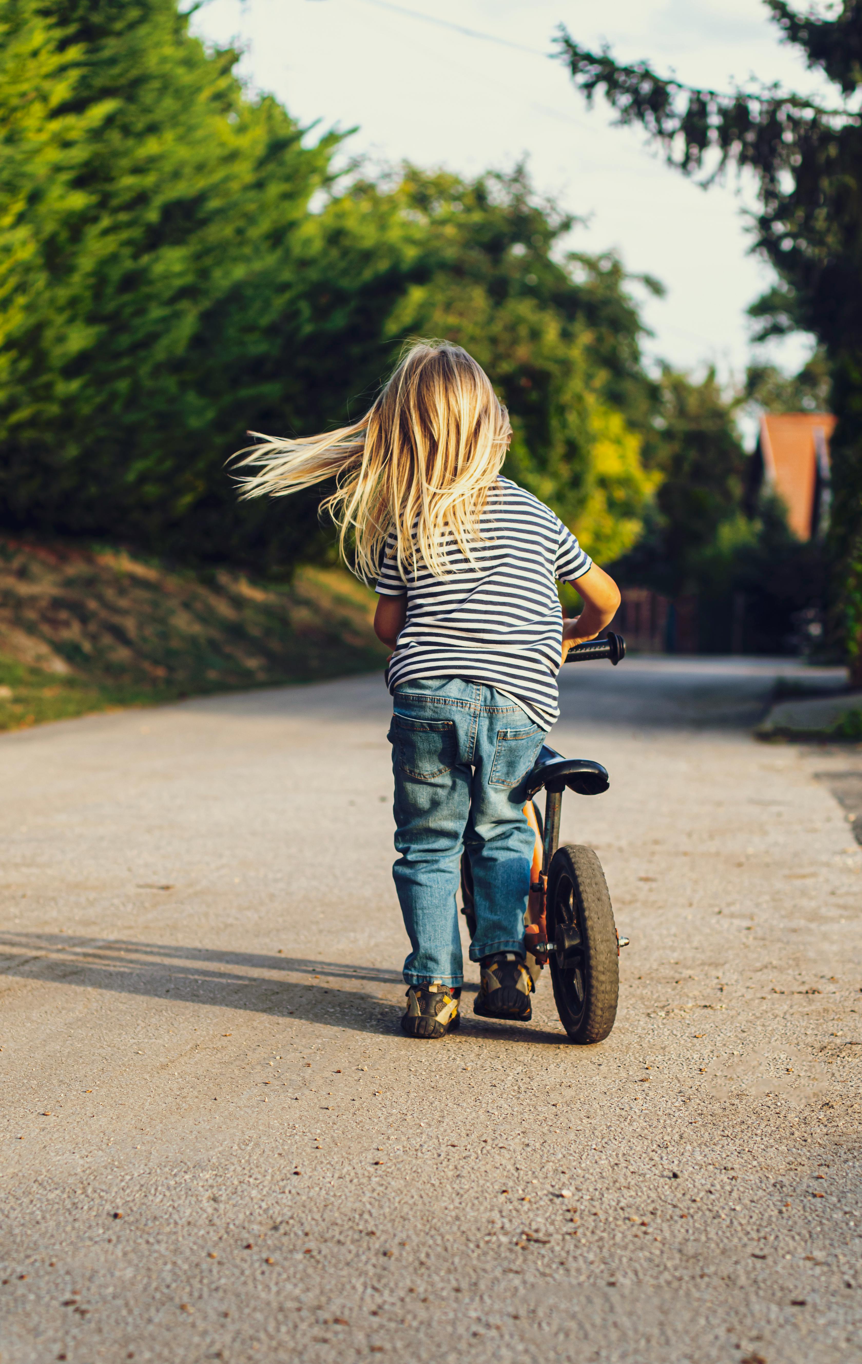 Anonymous kid in helmet riding run bike on pavement in countryside ...
