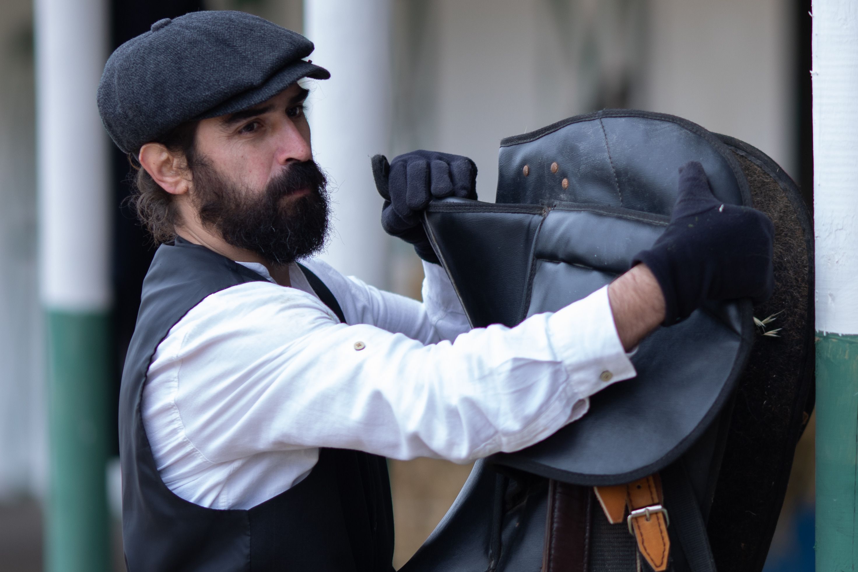 Bearded Brunette in Flat Hat Holding Saddle · Free Stock Photo
