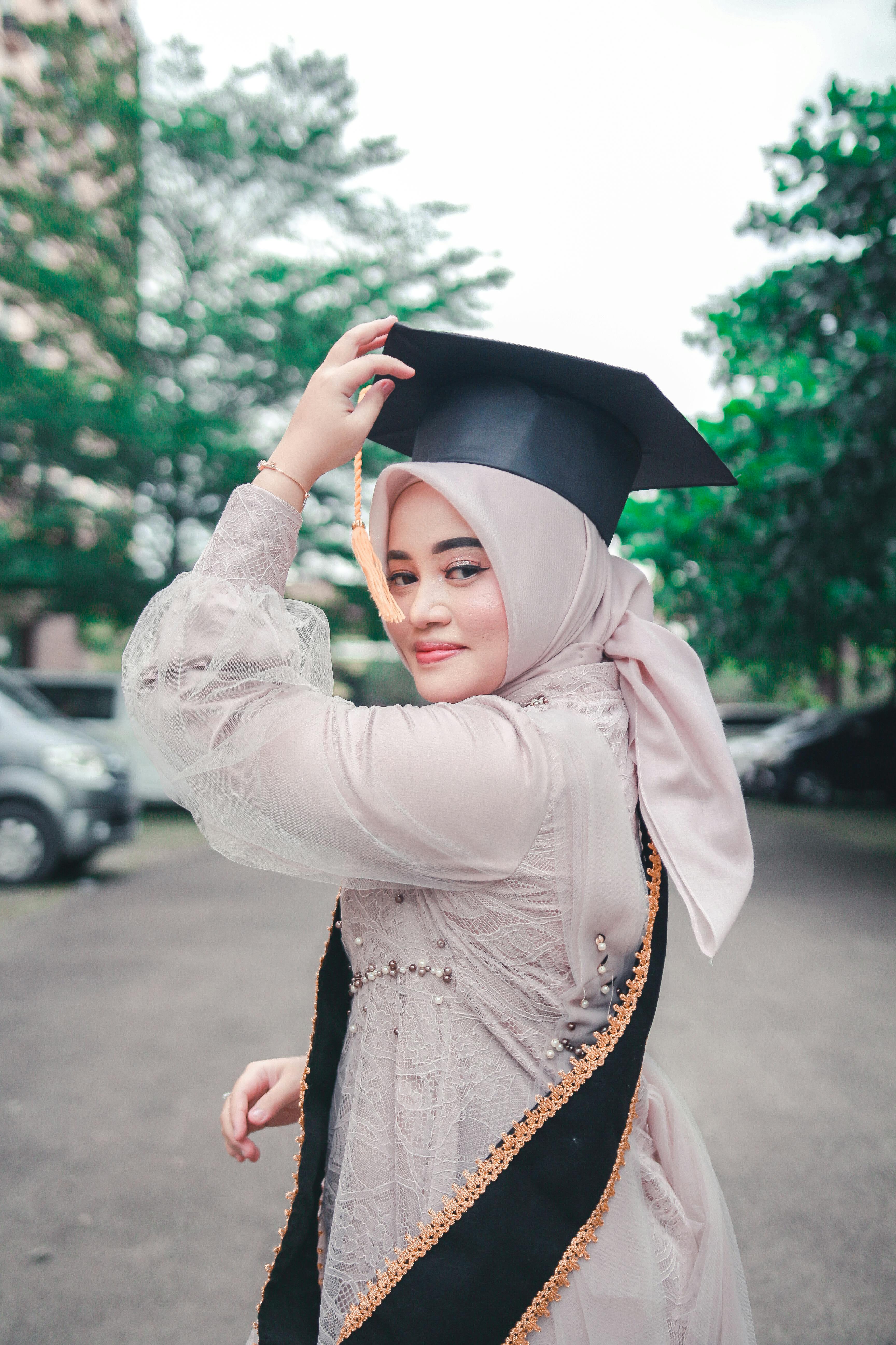 Graduate in Hijab and Gown Holding Academic Hat near Walls of Anitkabir ...
