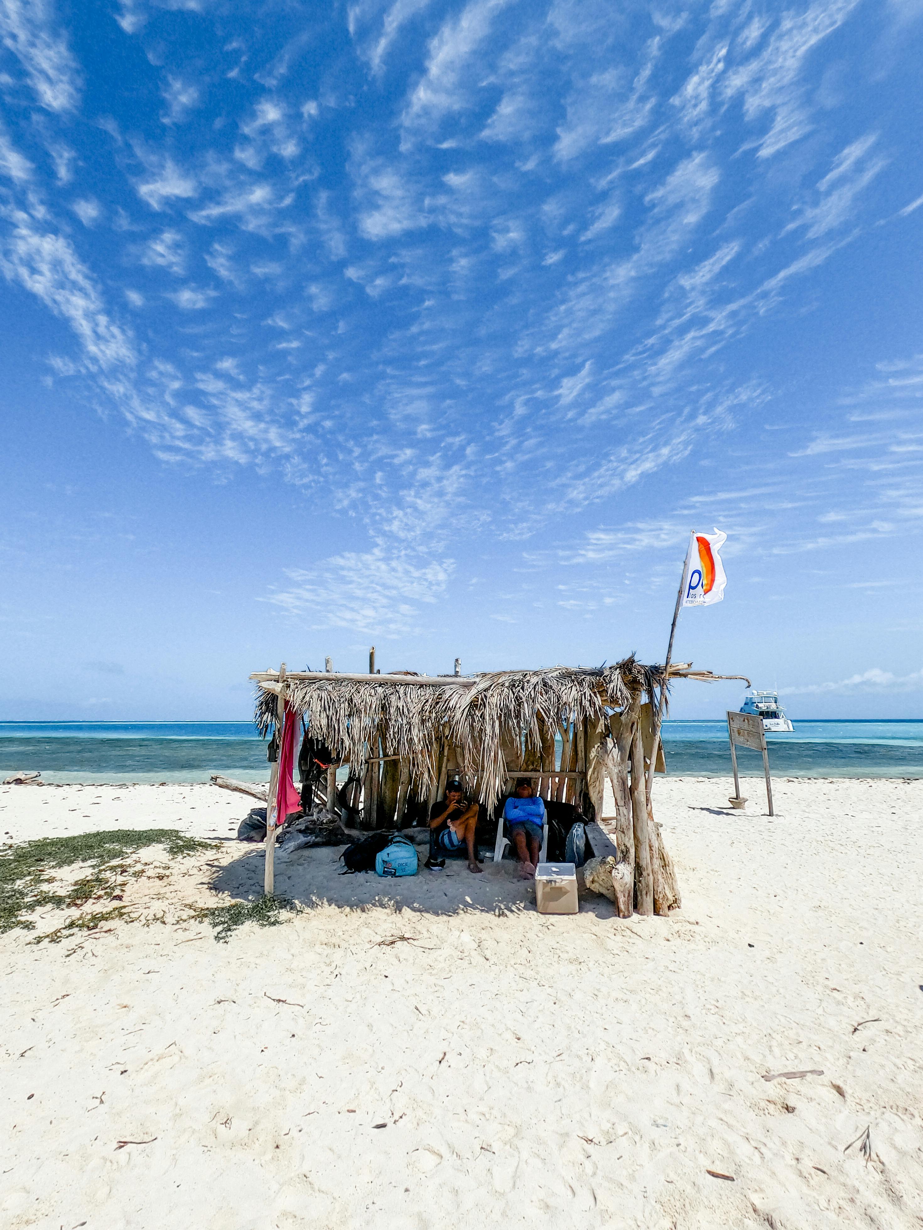 A hut on the beach with people sitting on it · Free Stock Photo
