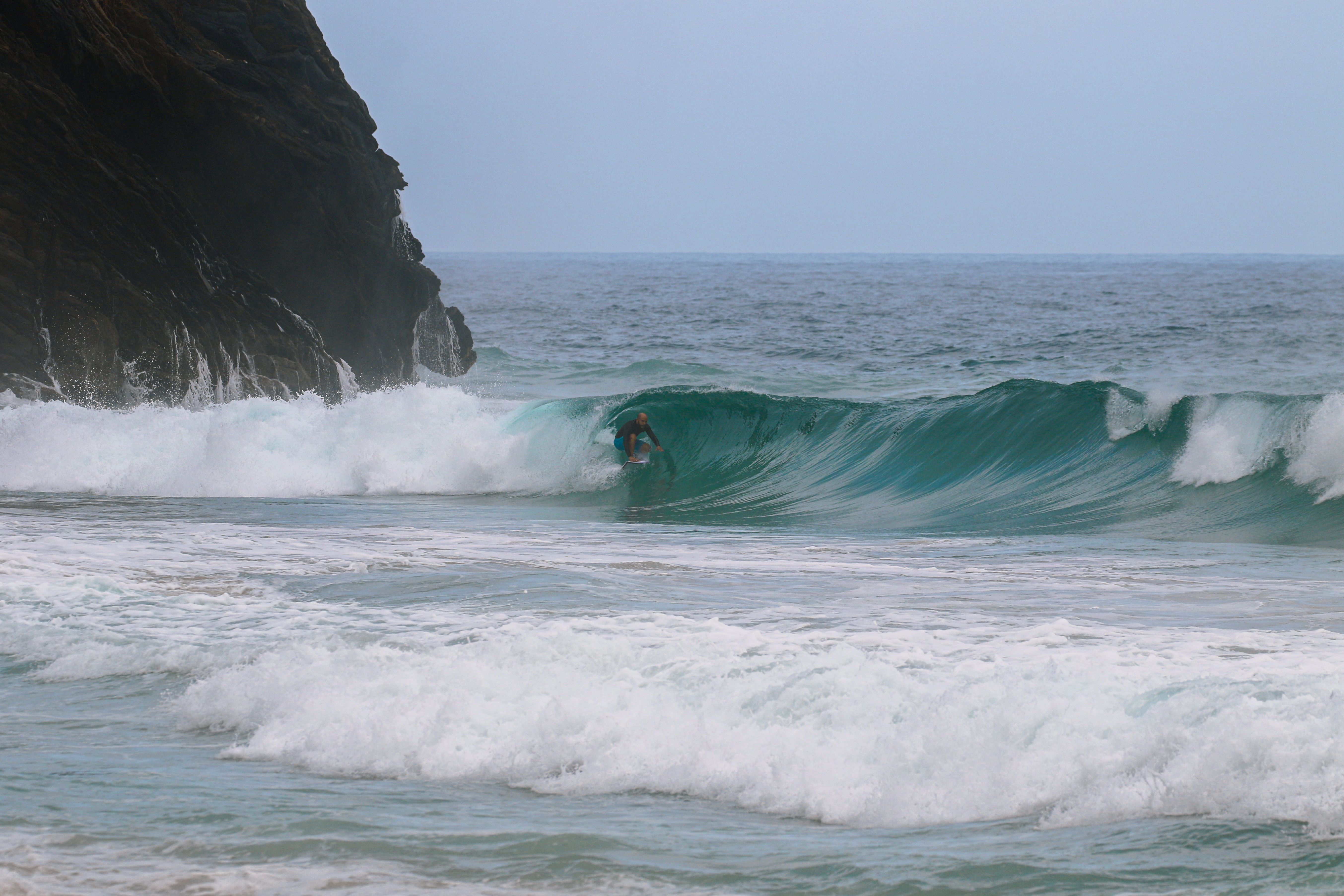 A surfer rides a wave in front of a cliff · Free Stock Photo