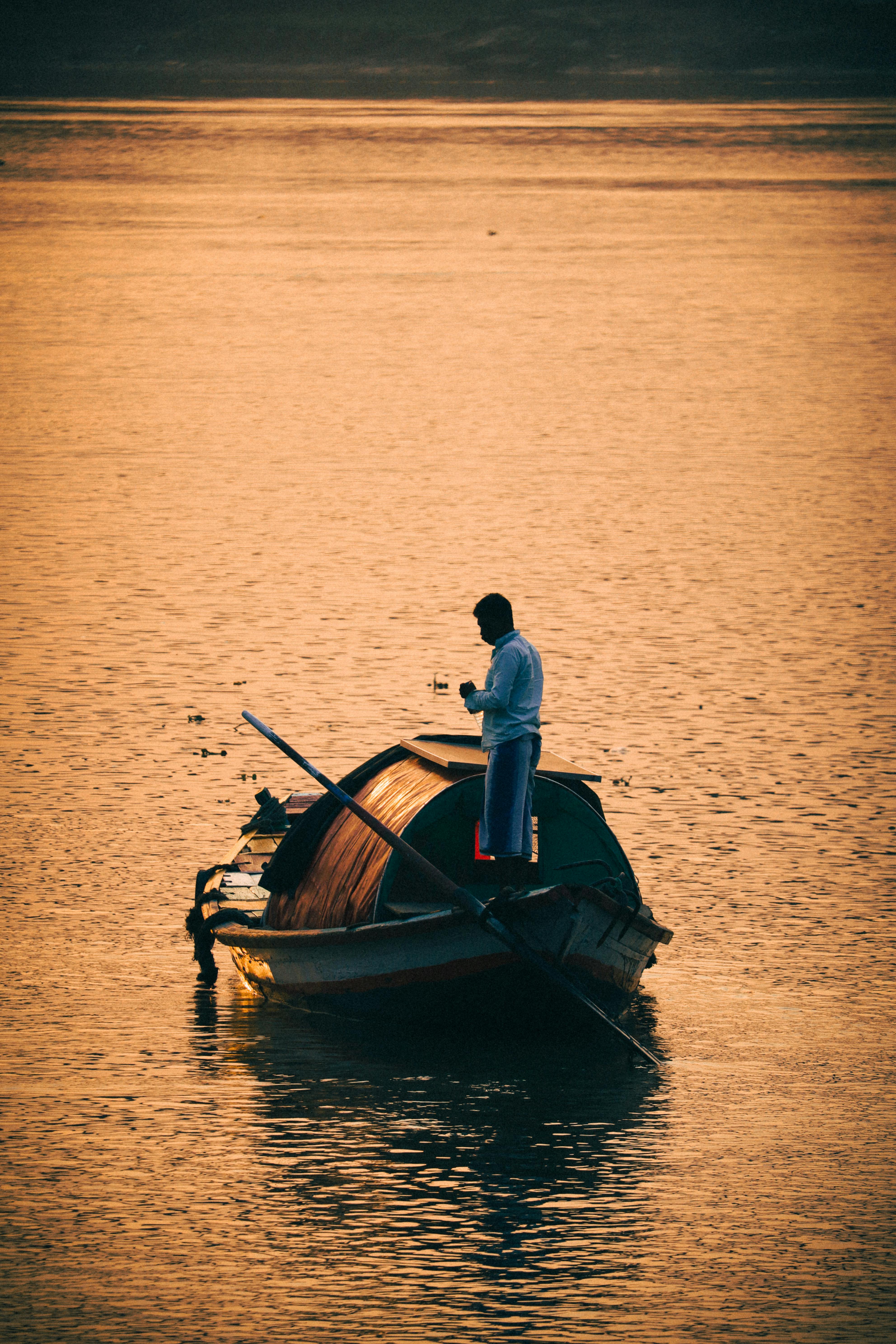 Man Standing on a Small Wooden Boat at Sunrise · Free Stock Photo