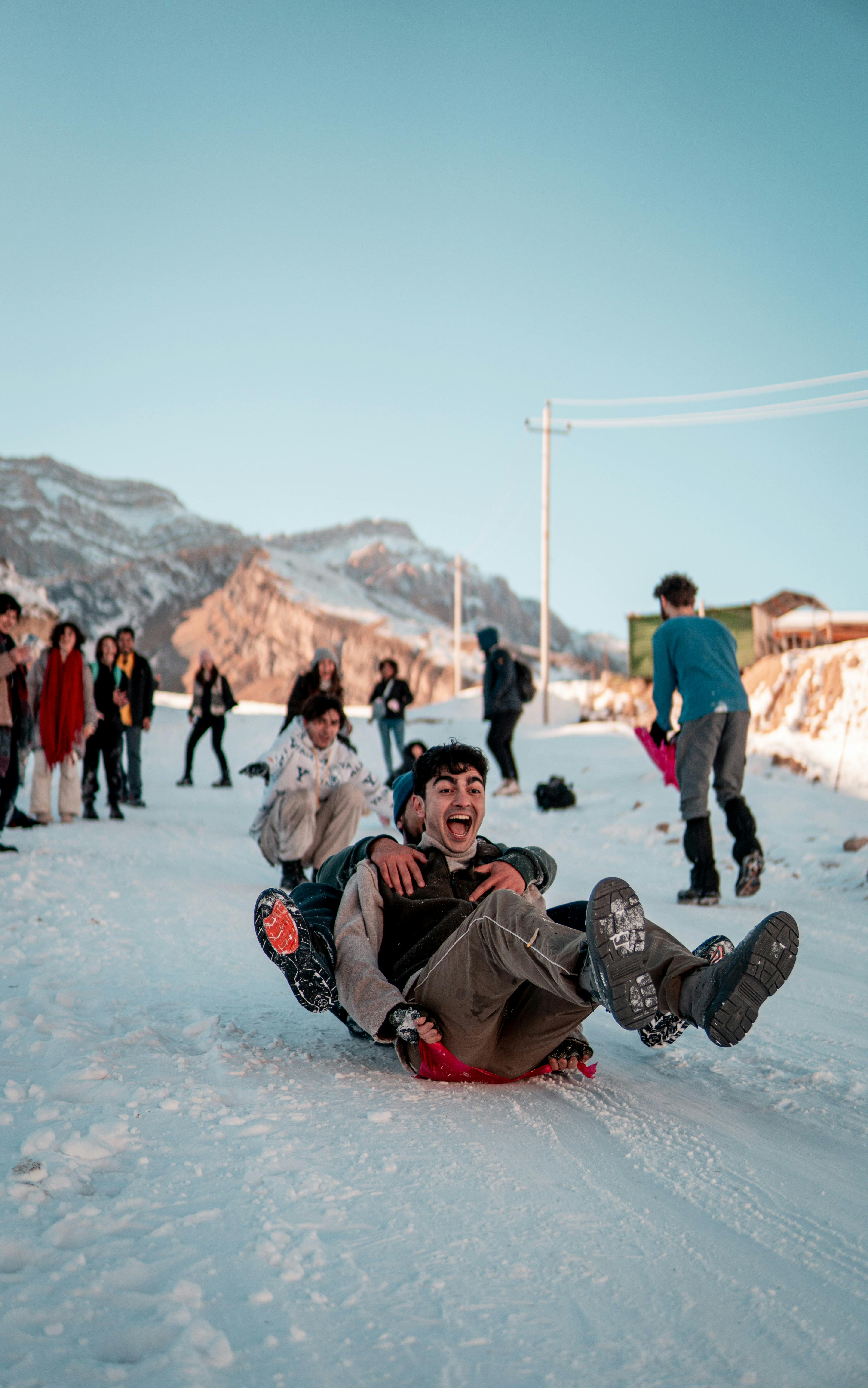 People sledding down a snowy hill in the mountains · Free Stock Photo