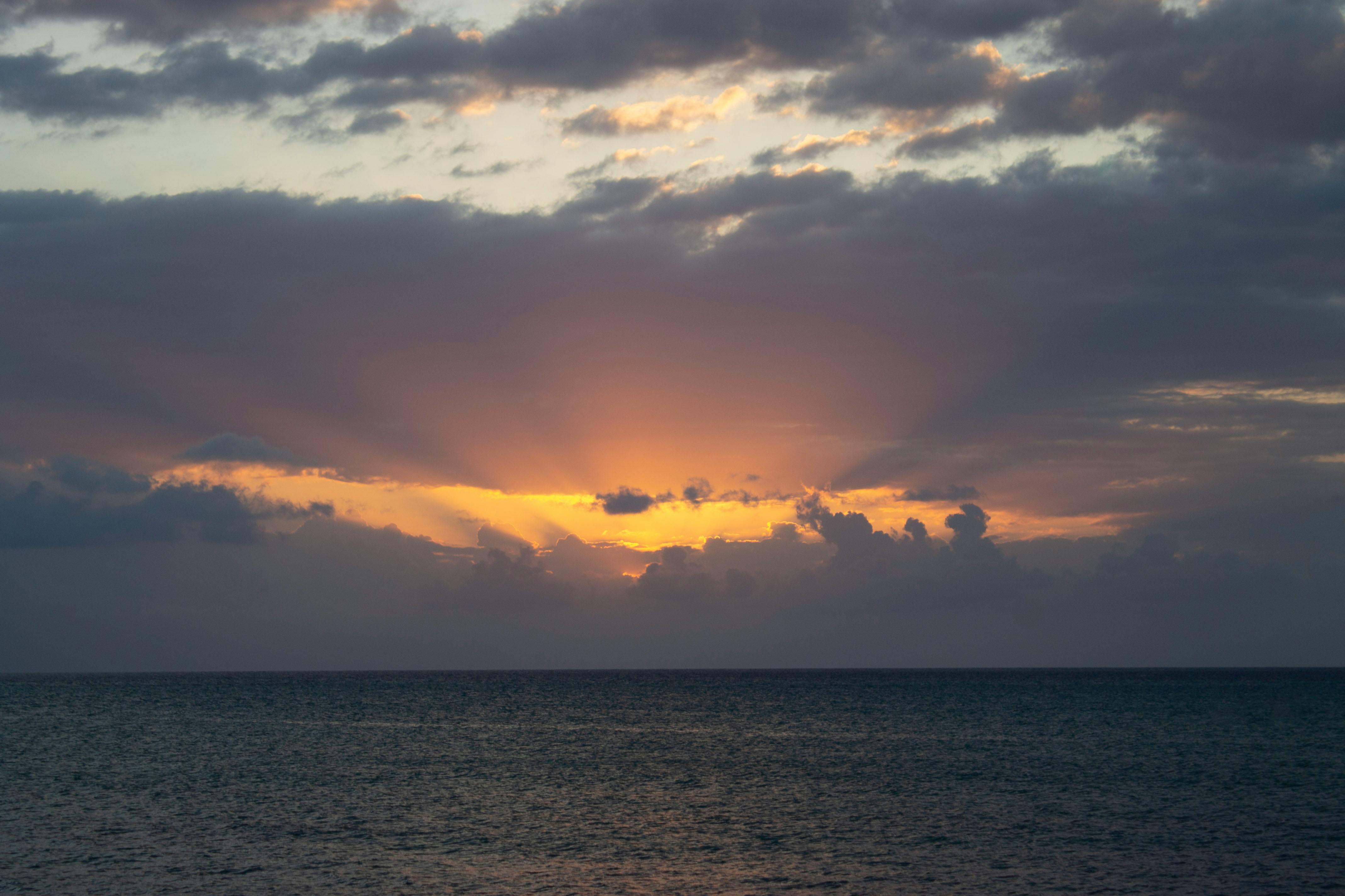 A sunset over the ocean with clouds and sun rays · Free Stock Photo
