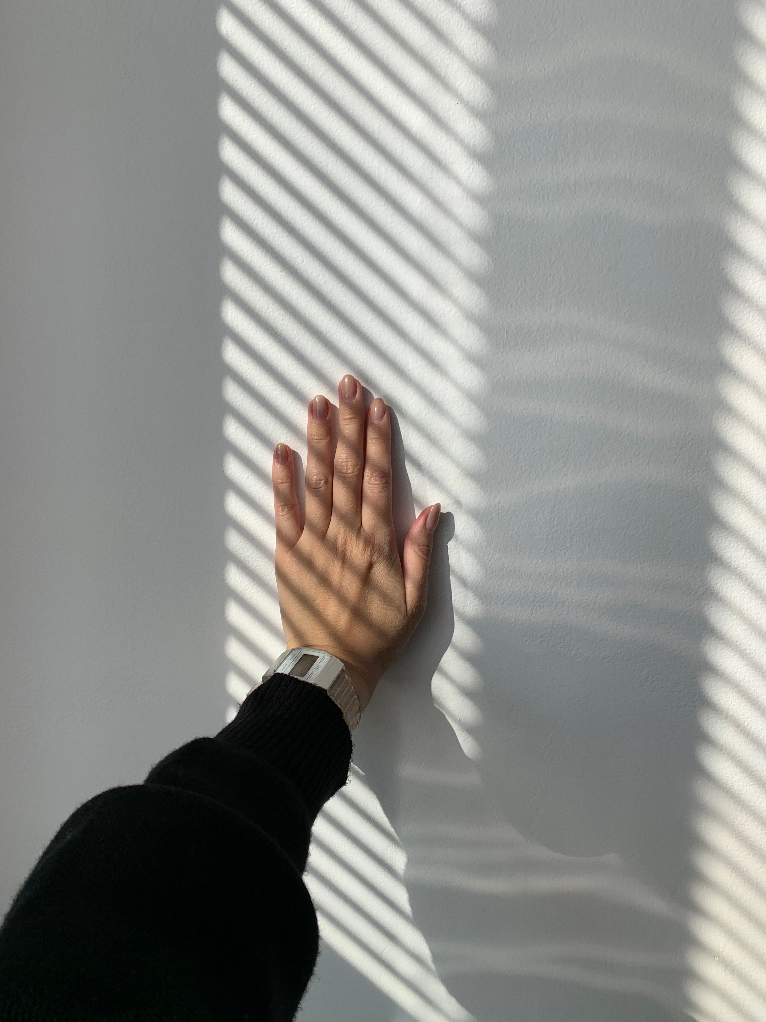 A person's hand is touching the wall with the sun shining through the ...