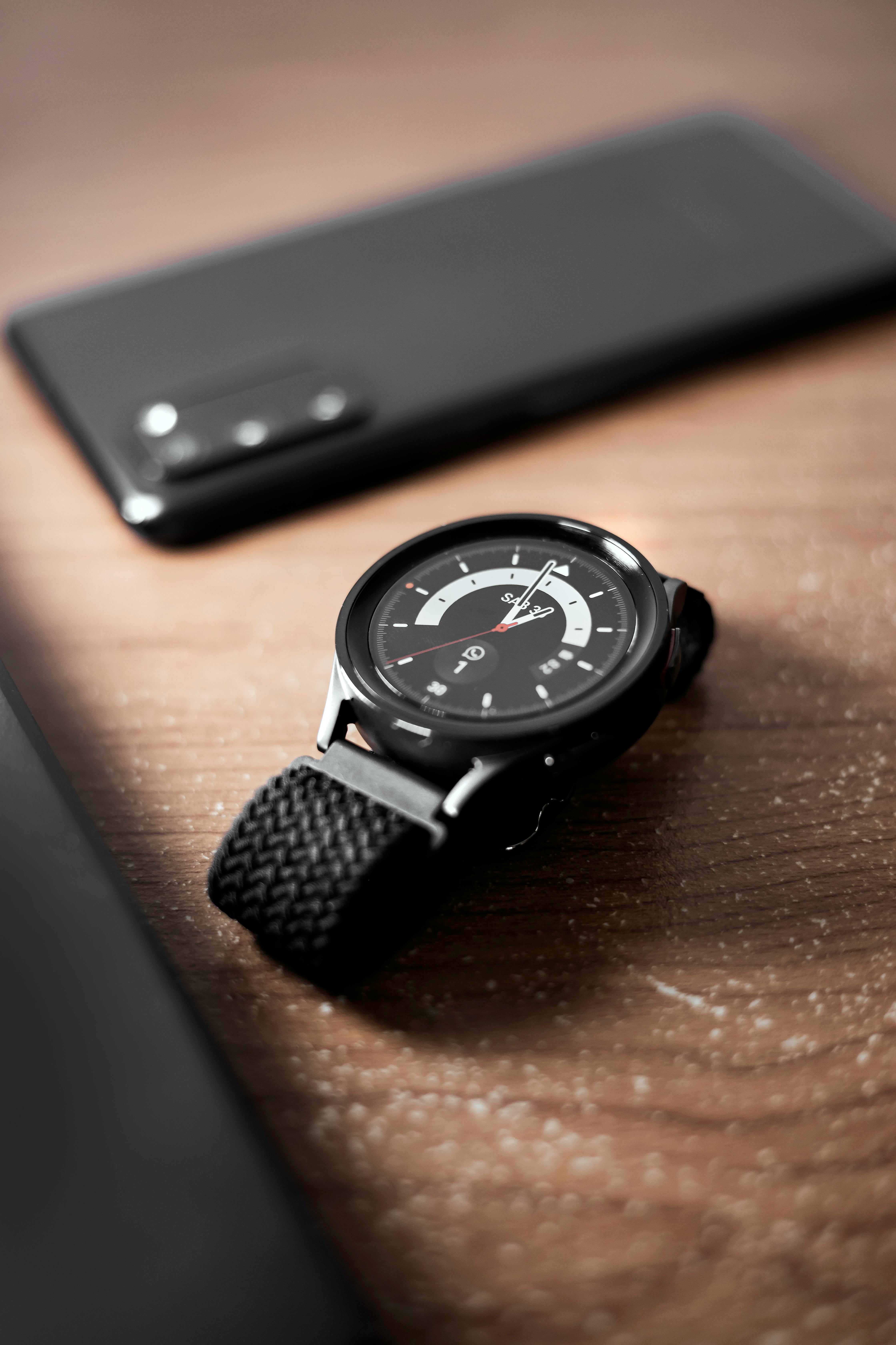 Red Smartphone Beside the Black Chronograph Watch on Brown Wooden Board ...