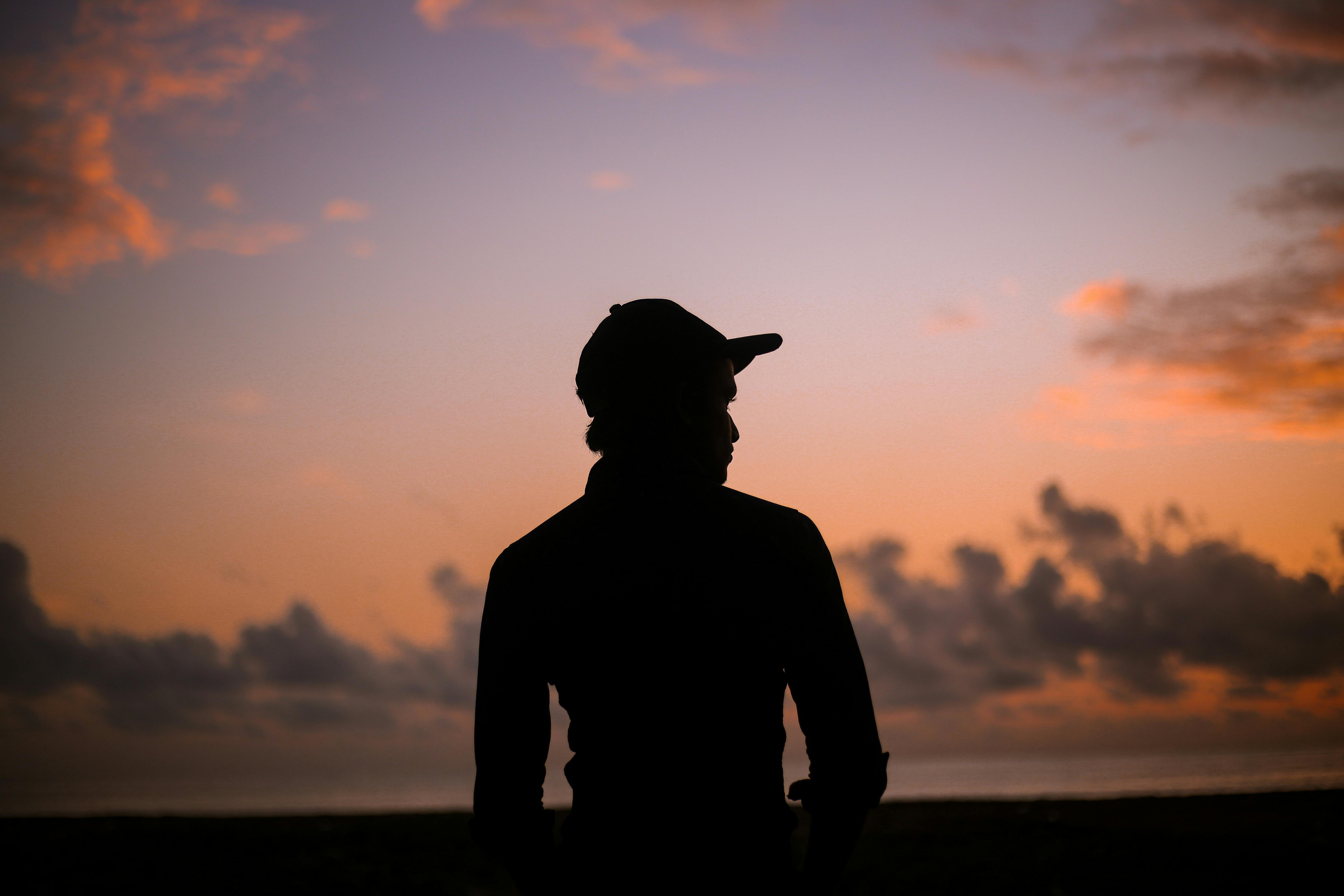 Silhouette of Man in Cap Standing by Wall at Sunset · Free Stock Photo