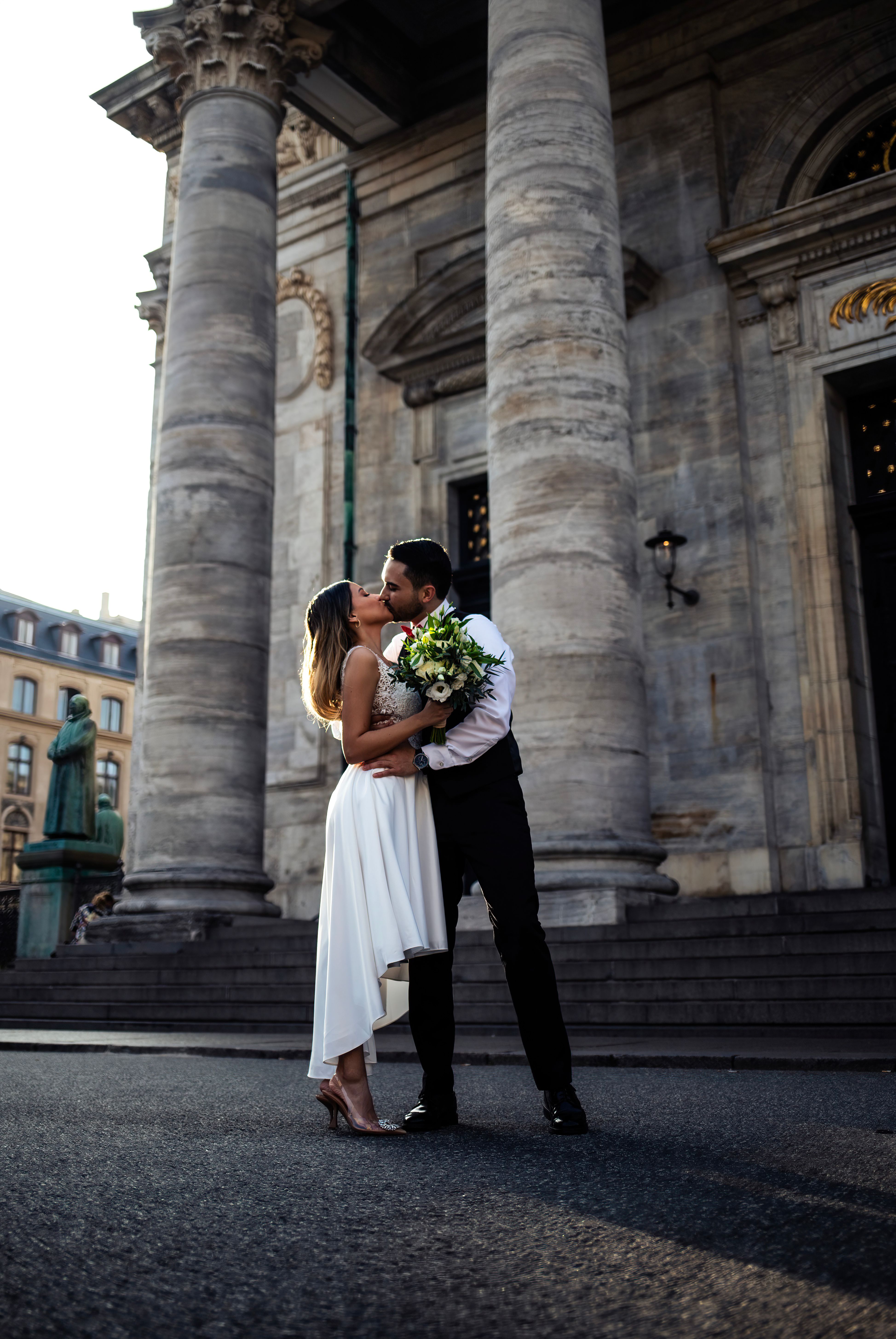 A bride and groom kiss in front of a large building · Free Stock Photo