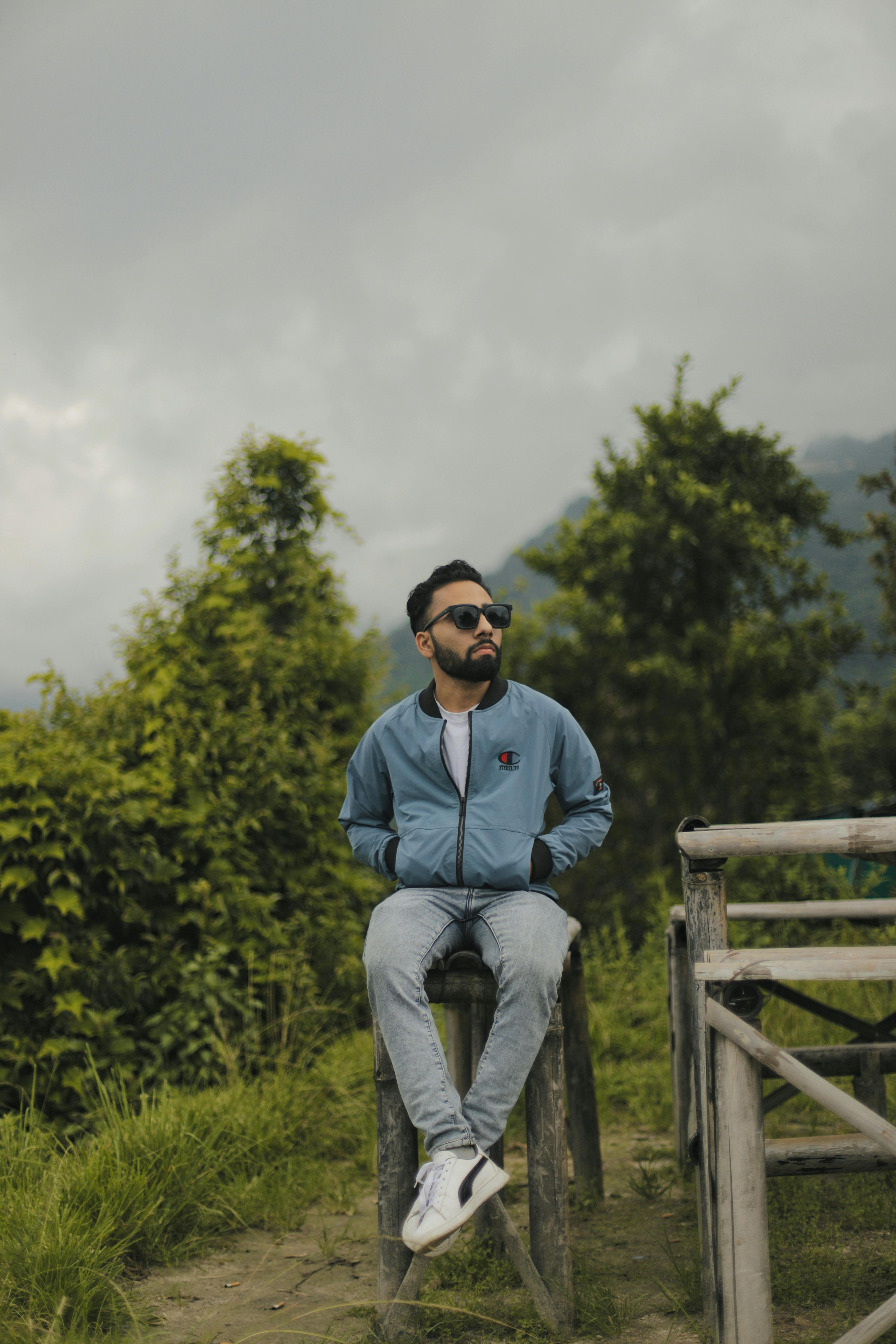 Man in a Jacket and Sunglasses Sitting Outside · Free Stock Photo