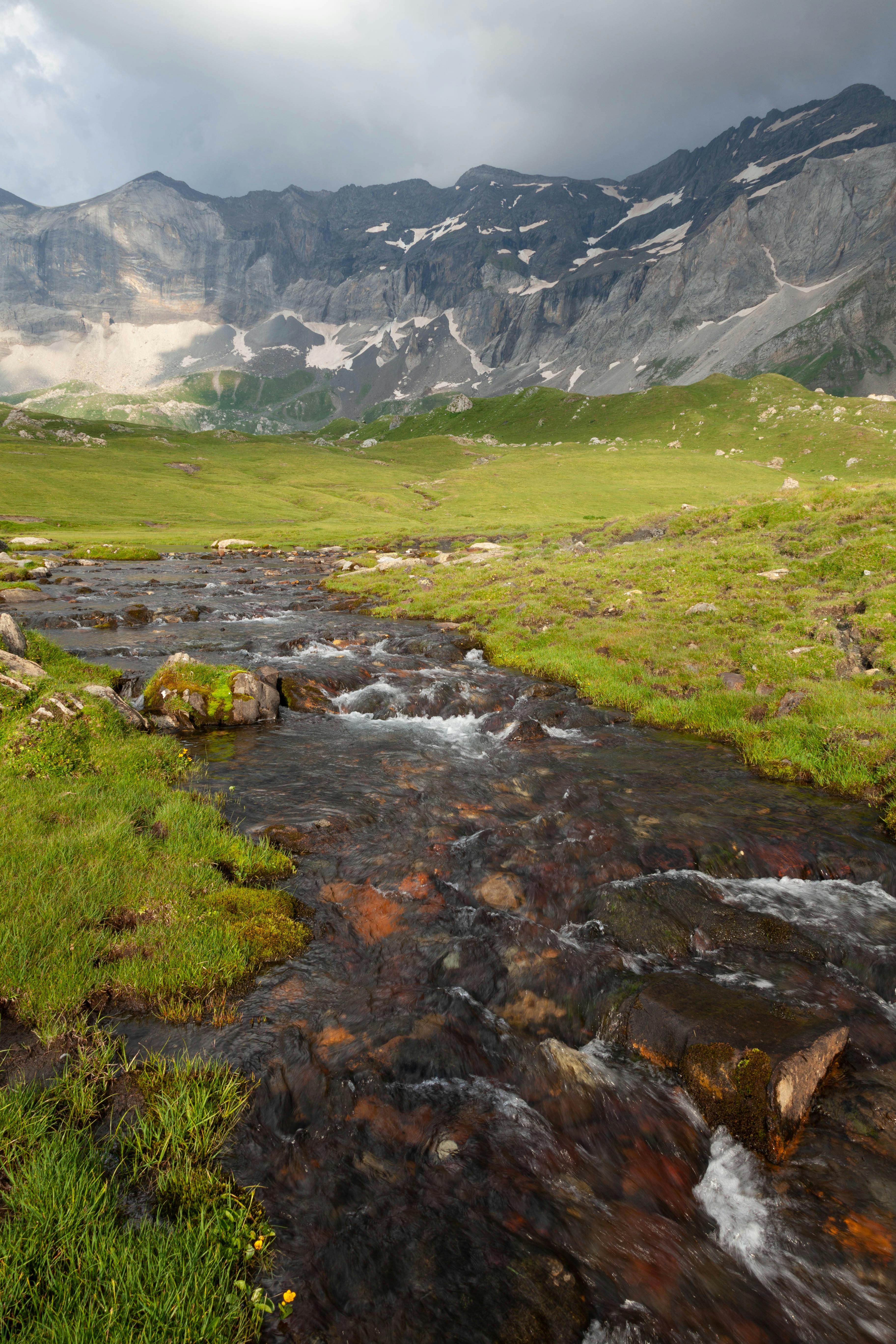 A stream runs through a grassy field with mountains in the background ...