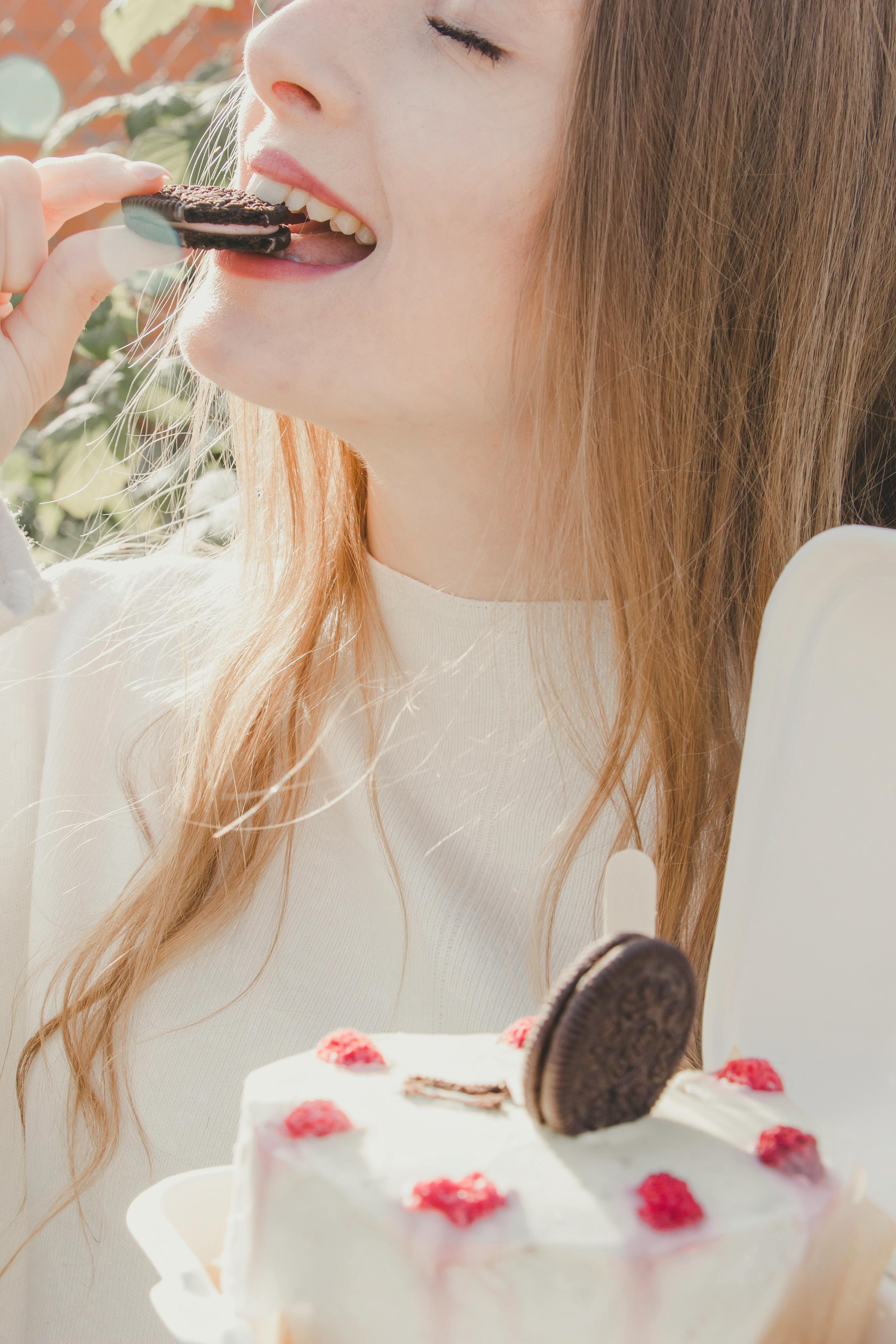 Woman Eating a Cookie from a Cream Cake Topped with Sandwich Biscuits ...