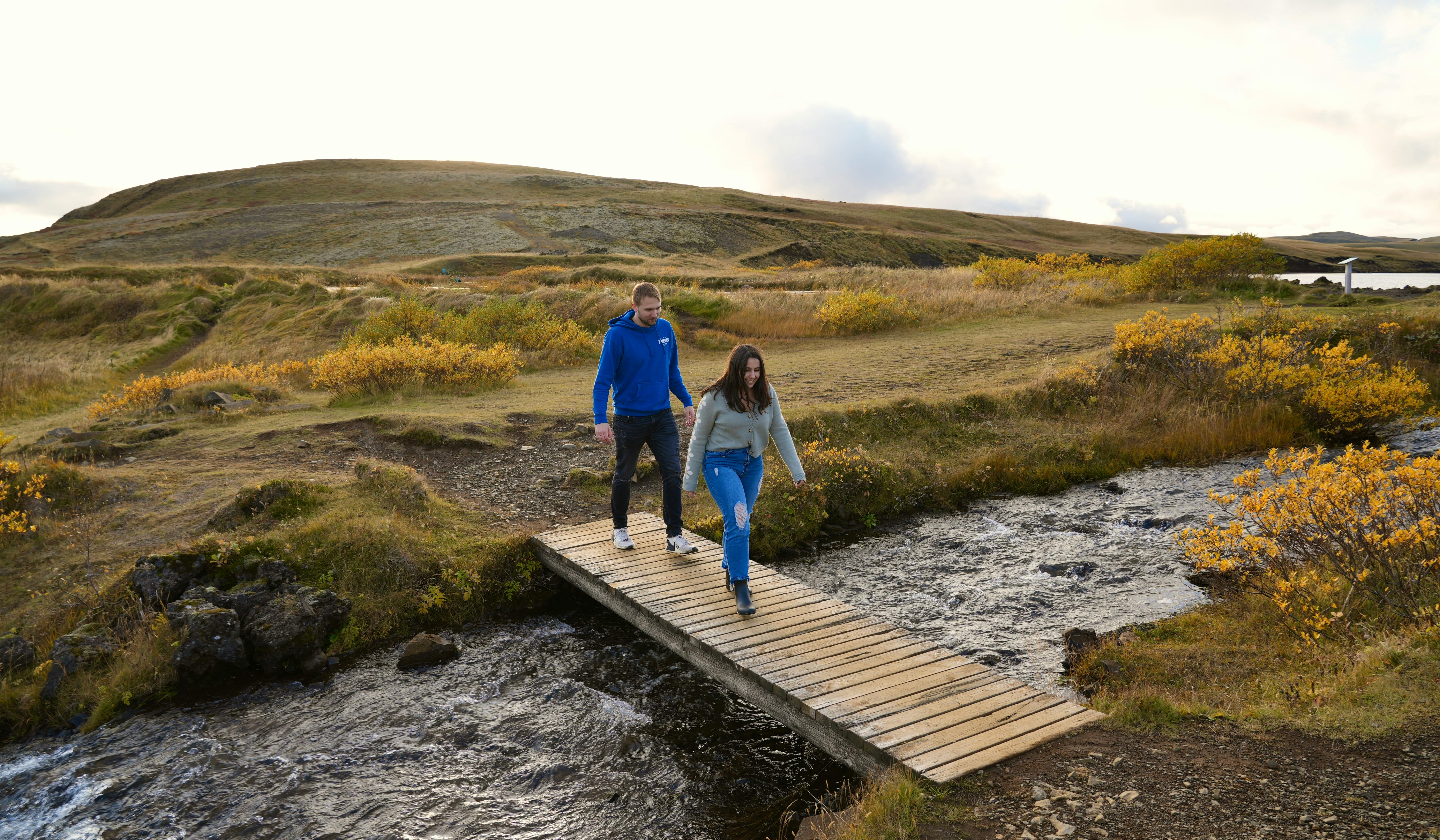 A couple walking across a bridge over a stream · Free Stock Photo