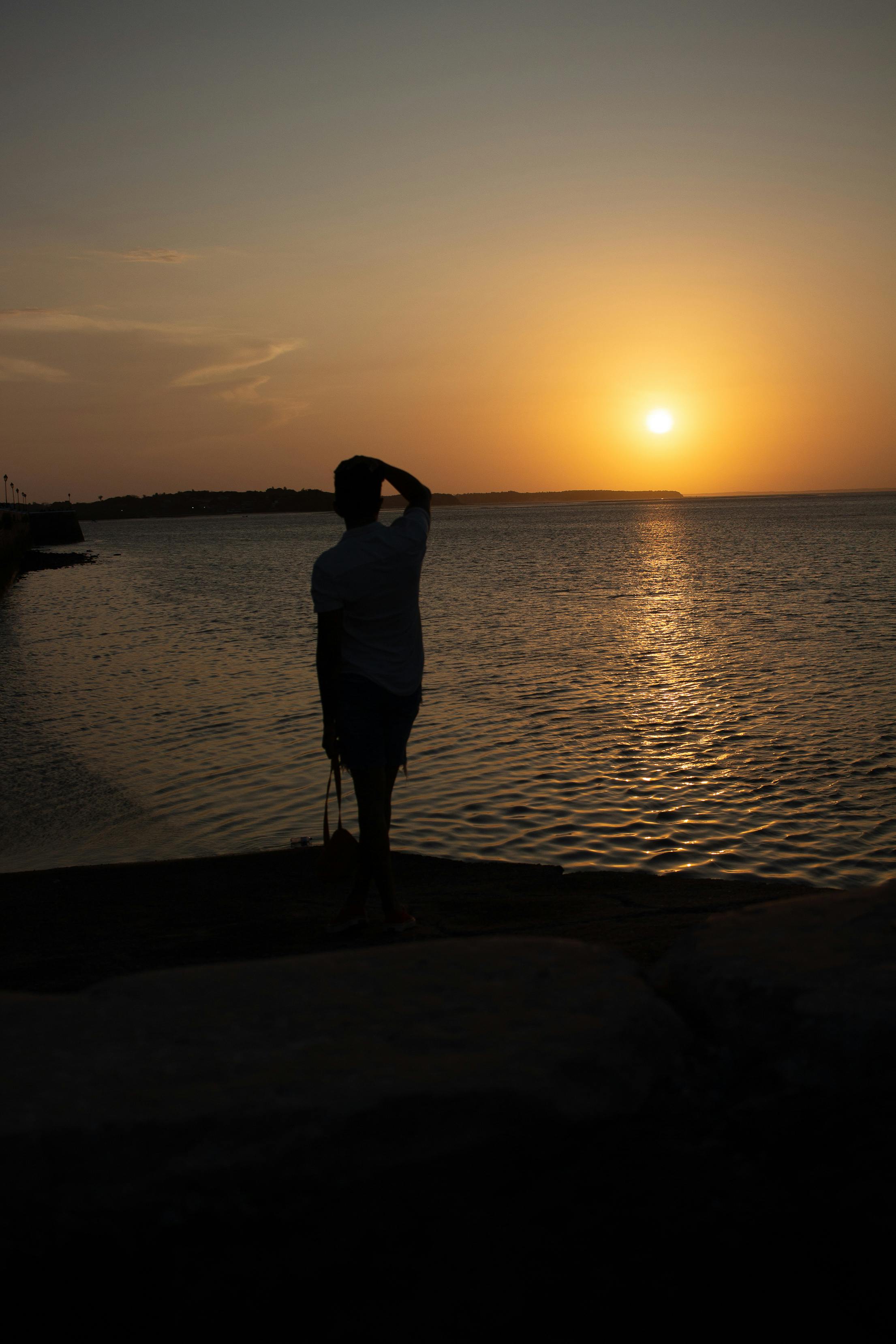 Silhouette of Person Standing on Sea Shore at Sunset · Free Stock Photo