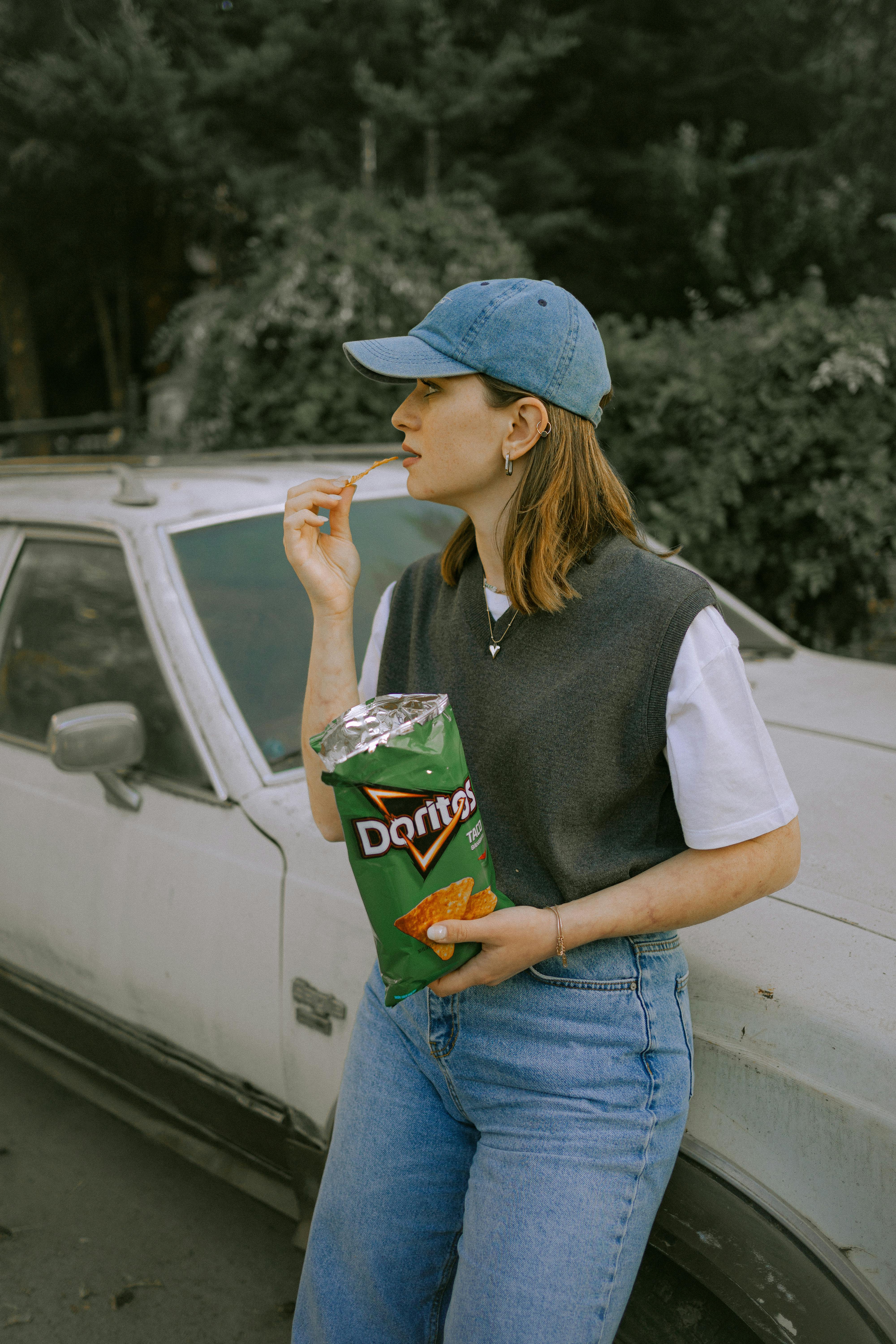 Portrait of Woman in Cap Eating Doritos · Free Stock Photo