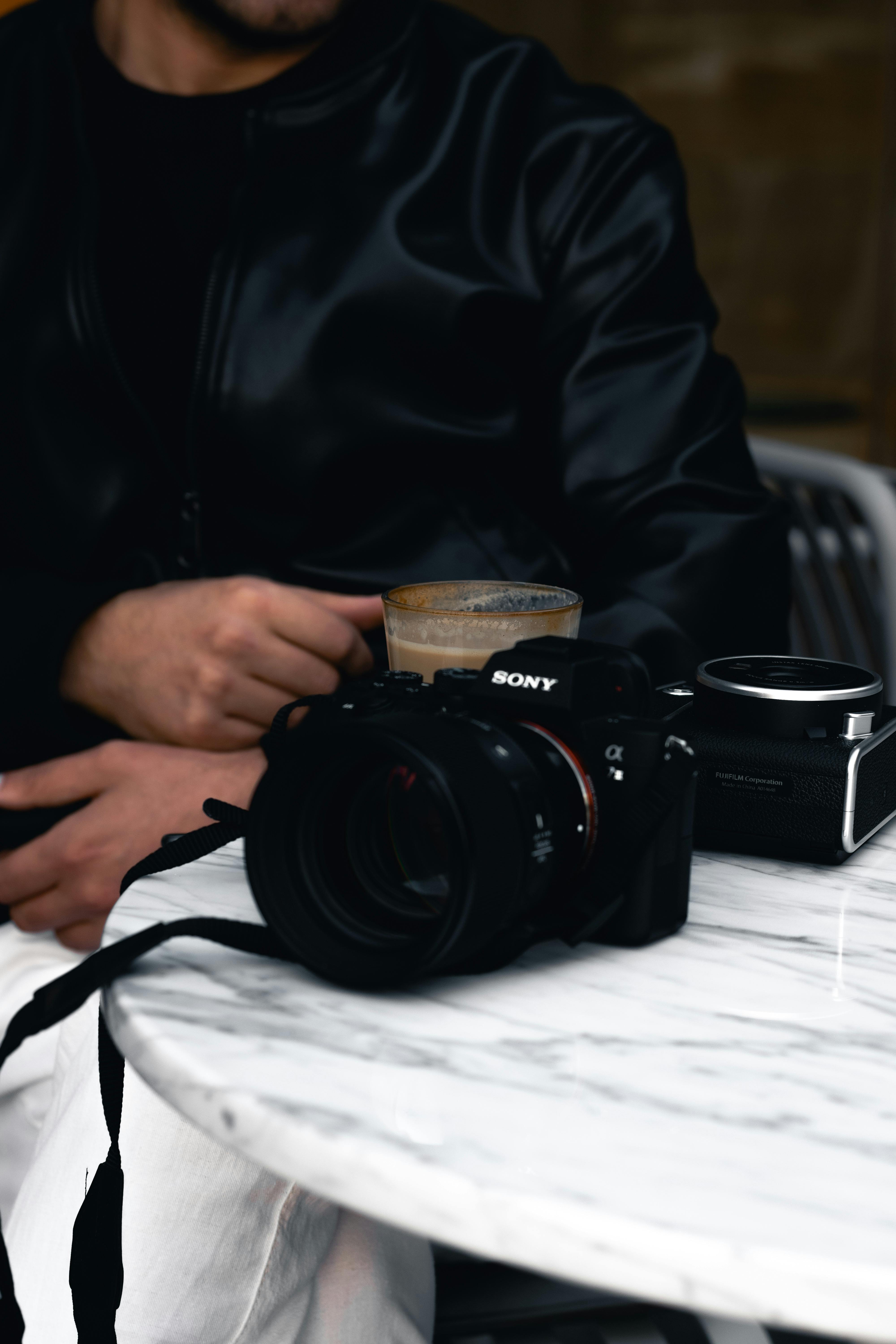 Photographer Drinking Coffee with his Cameras on a Table · Free Stock Photo