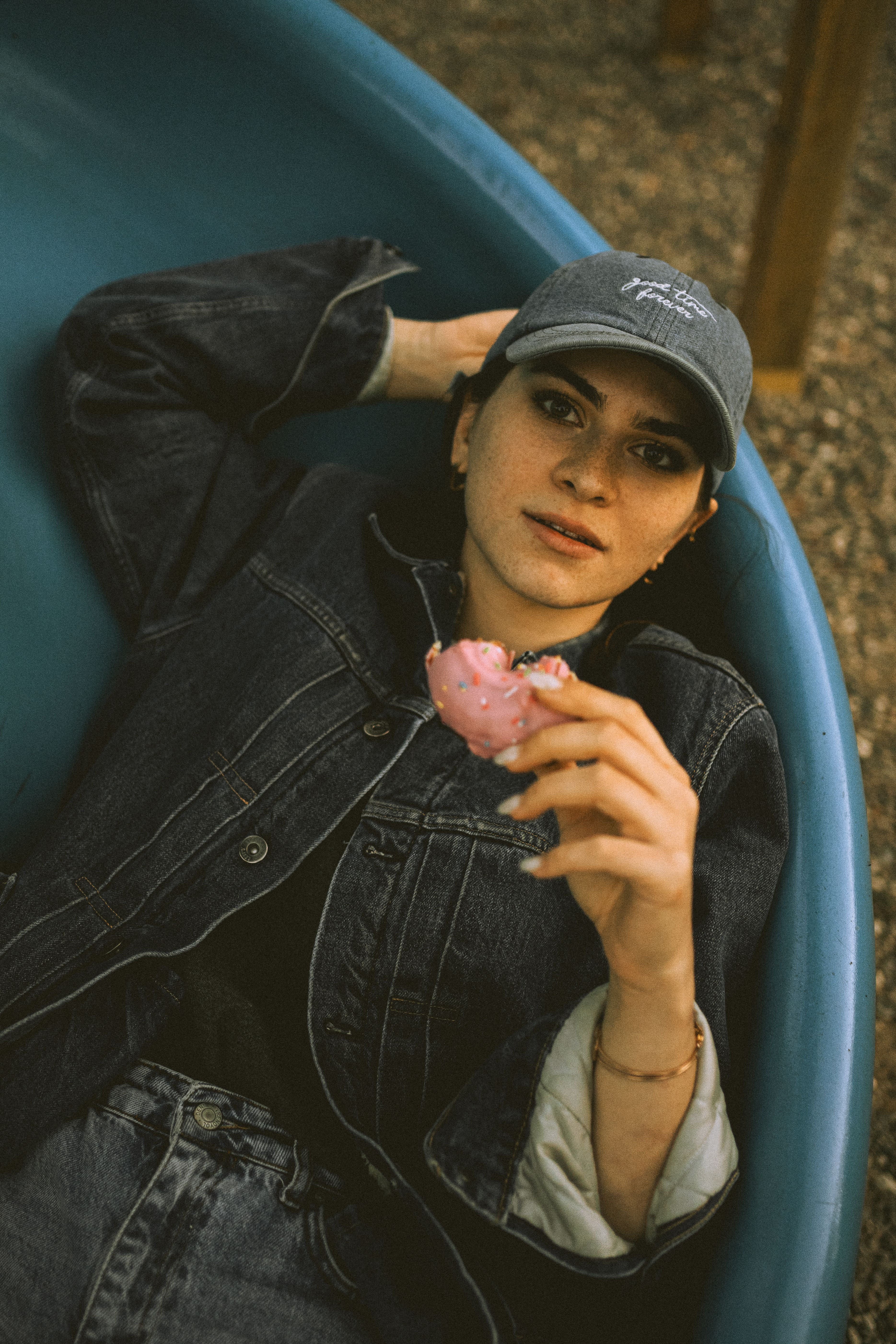 Young Woman in Denim Jacket and Baseball Cap Eating a Donut while Lying ...