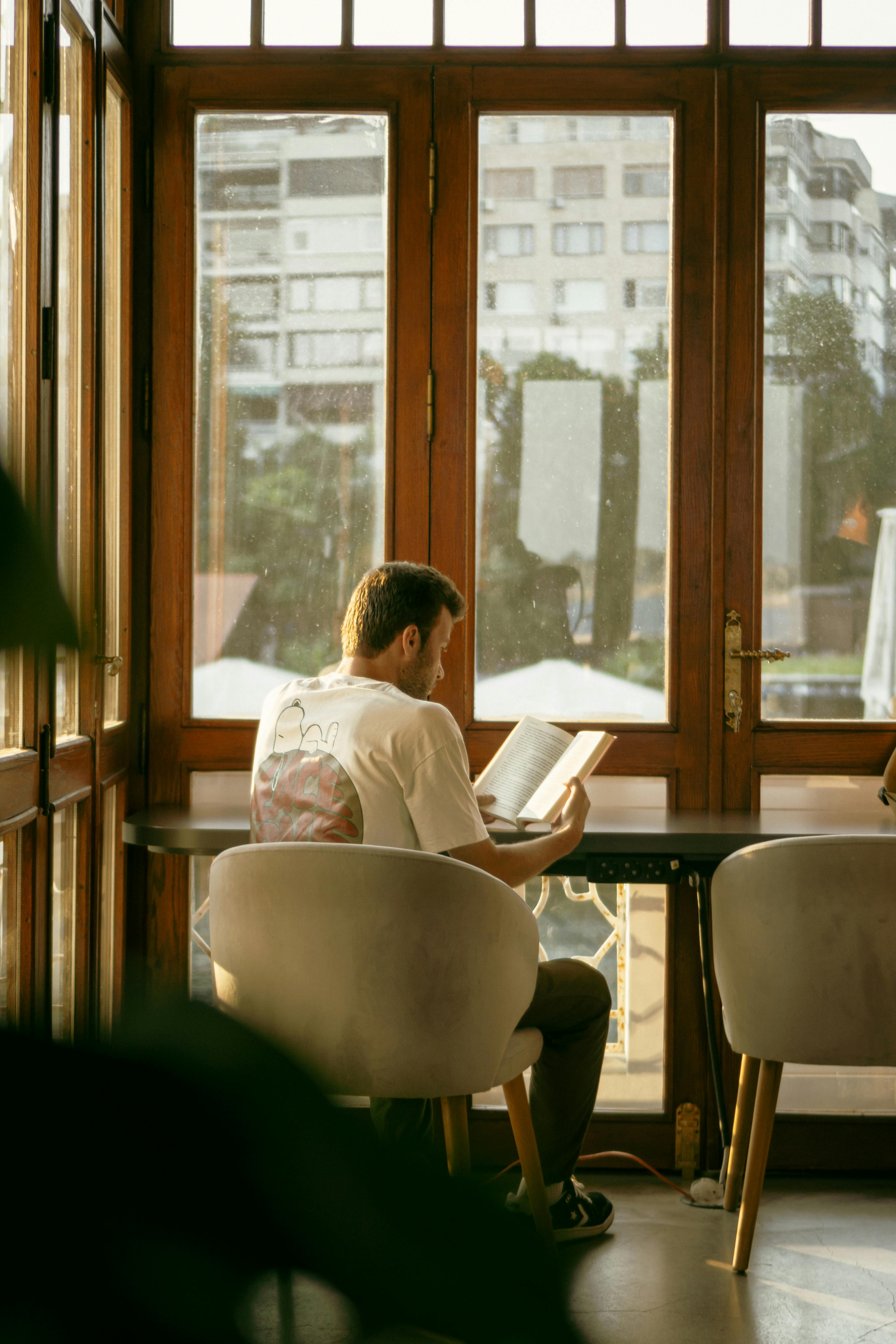 Man Sitting by Table and Reading Book · Free Stock Photo
