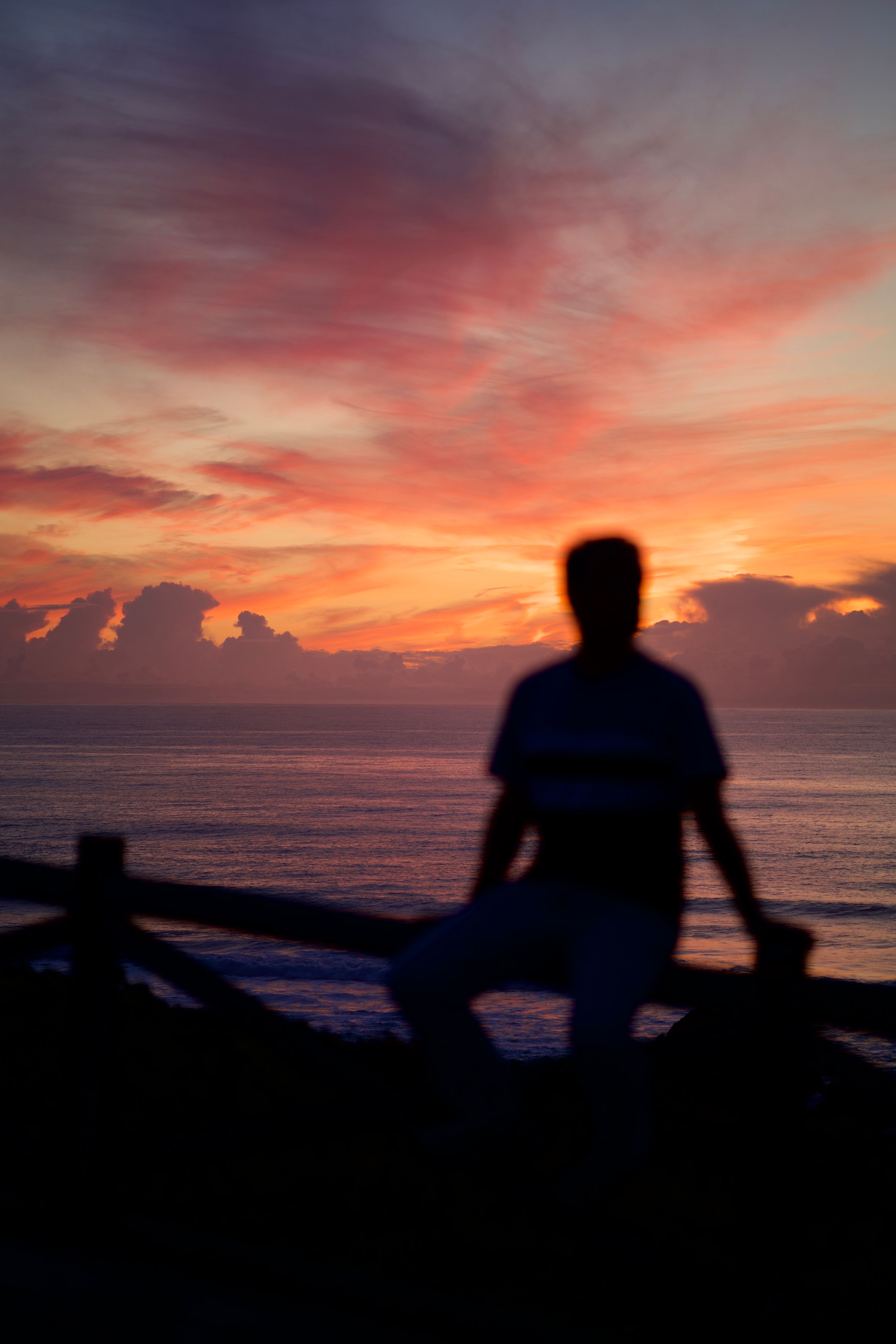 Silhouette of a Person Sitting on a Shore at Sunset · Free Stock Photo