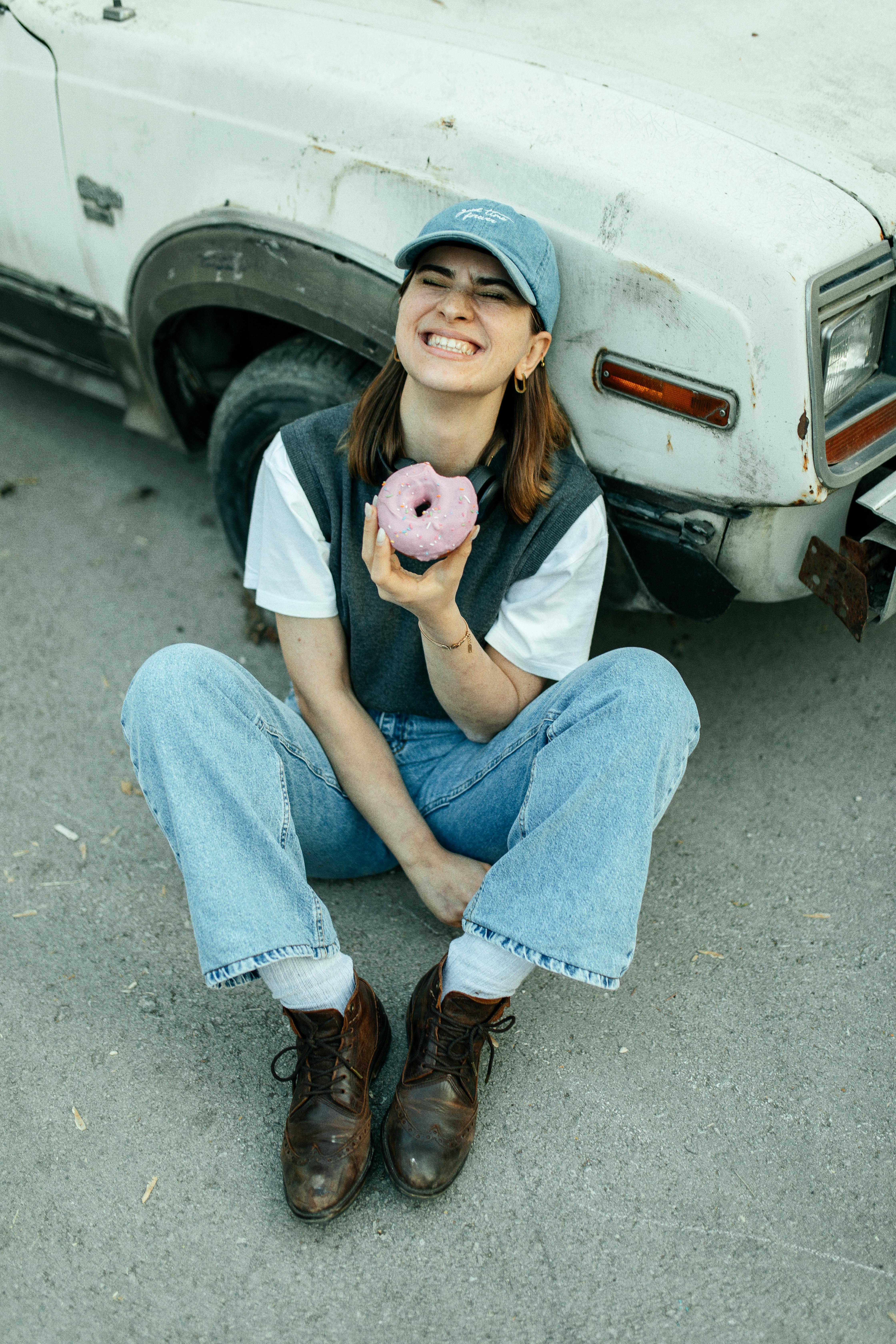 Laughing Woman Eating a Glazed Donut Sitting on the Asphalt Next to the ...
