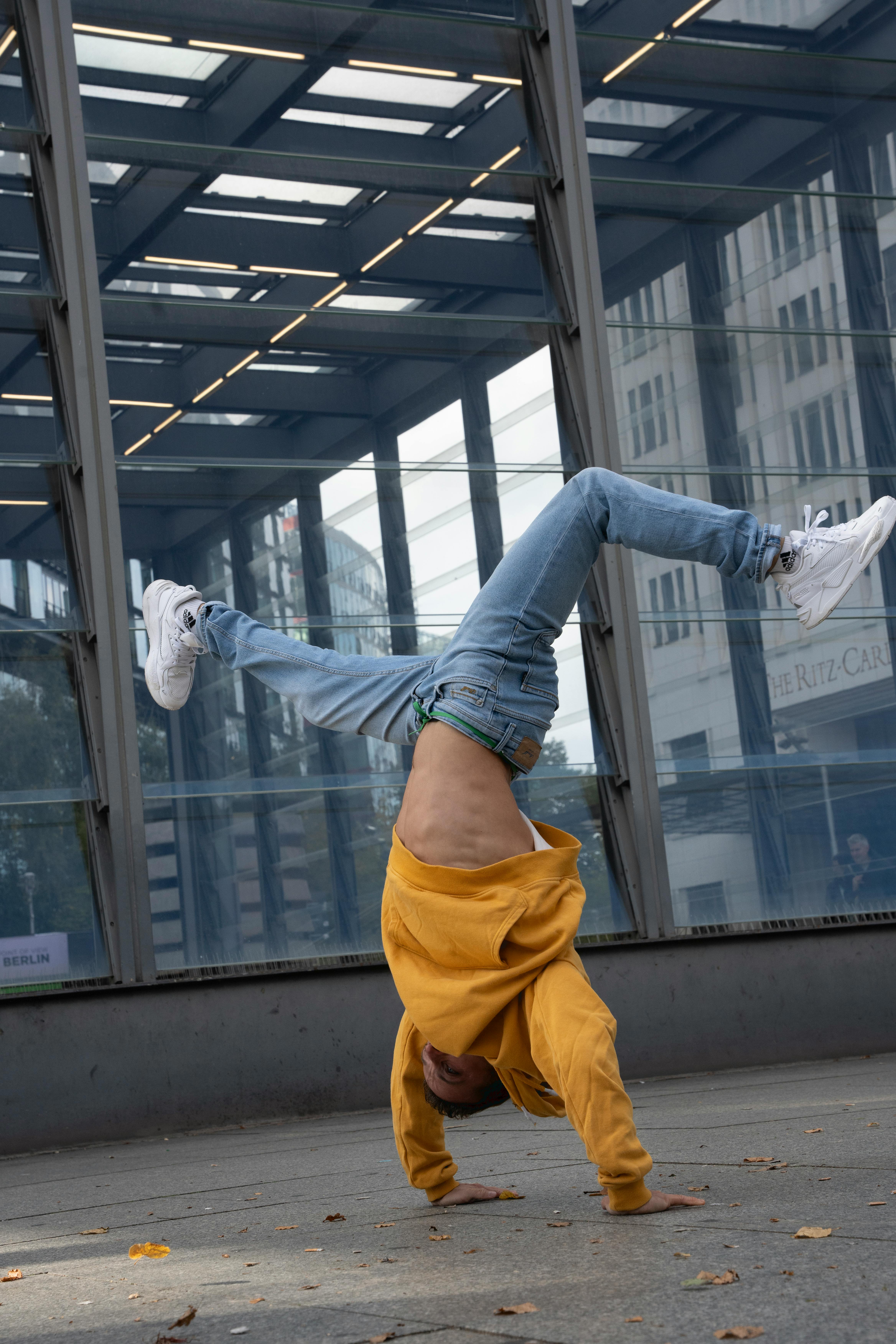 Man in Yellow Hooded Sweatshirt and Blue Jeans Standing on his Hands ...