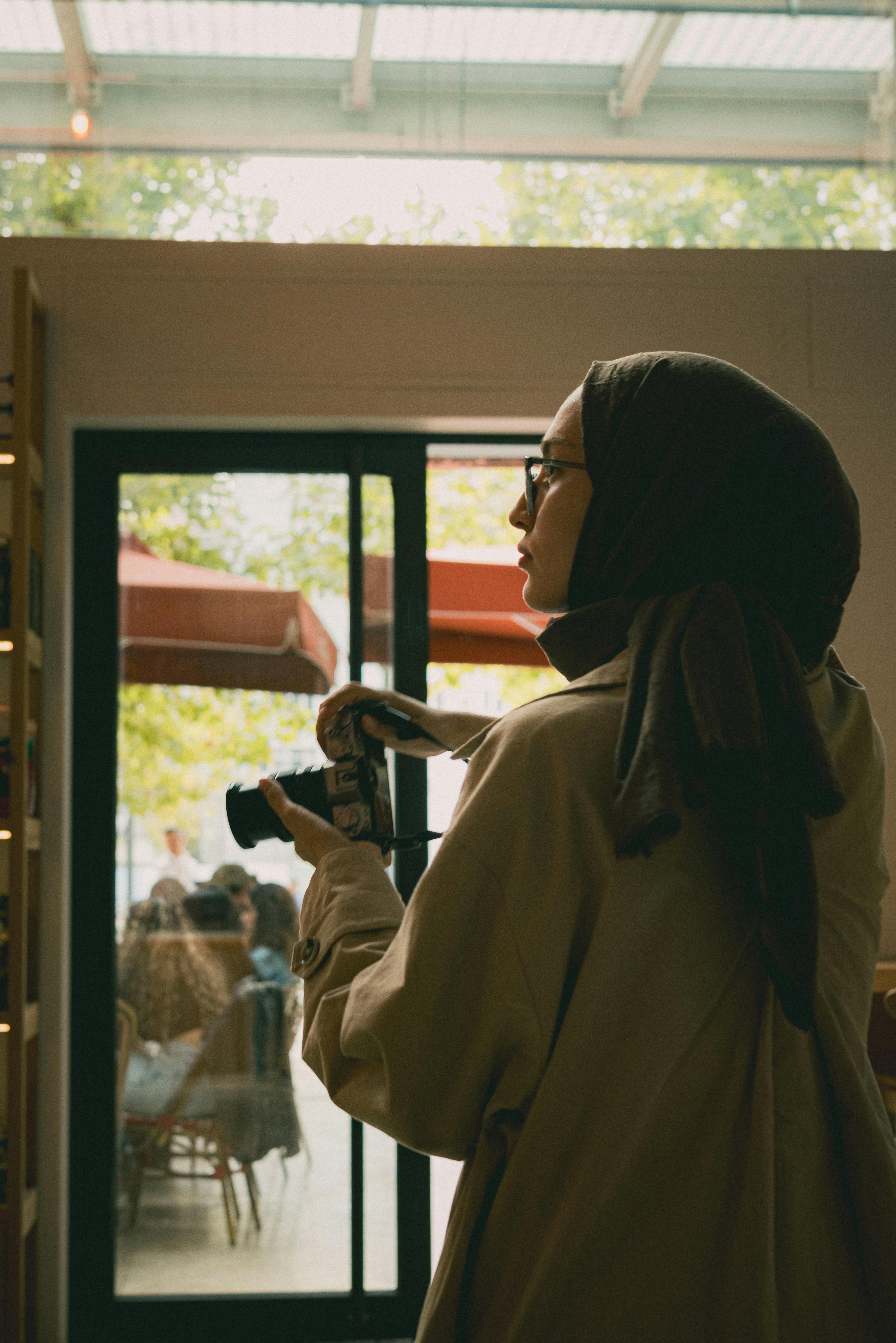 Young Woman Standing Inside with a Camera · Free Stock Photo